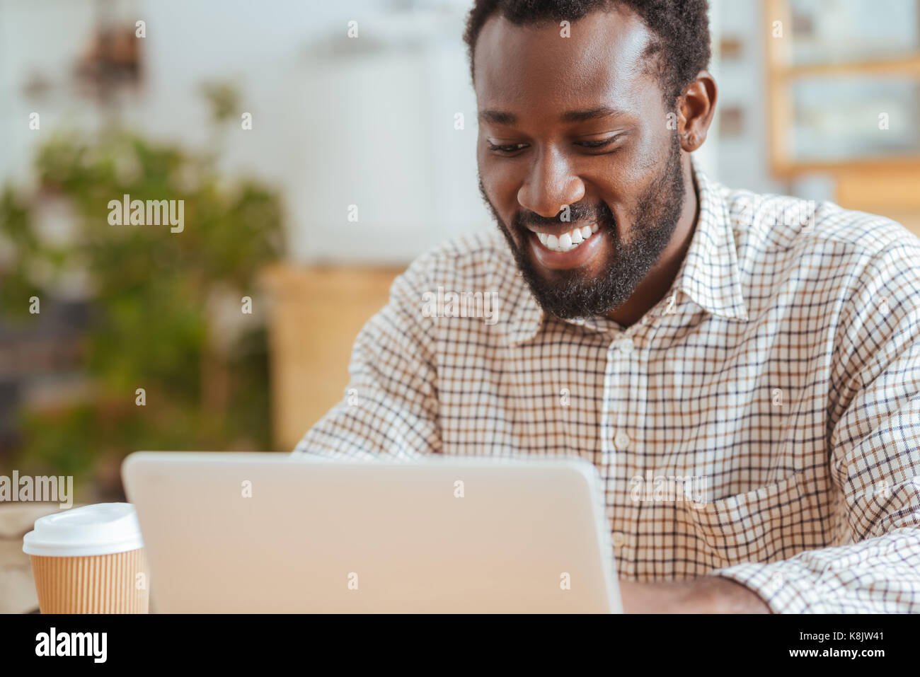 Pleasant cheerful man smiling while working on laptop Stock Photo - Alamy