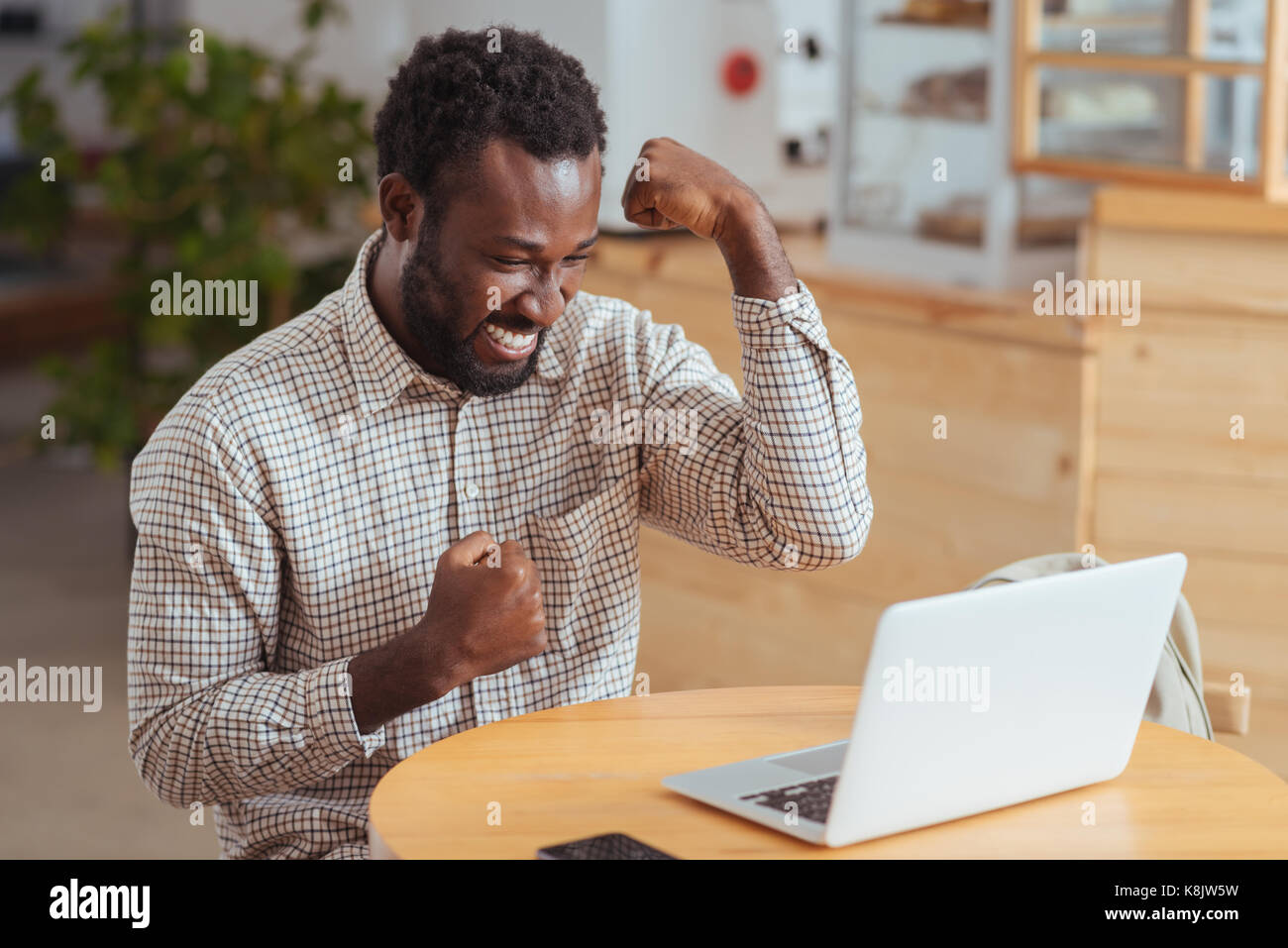 Overjoyed man raising hand in celebration while sitting in cafe Stock ...