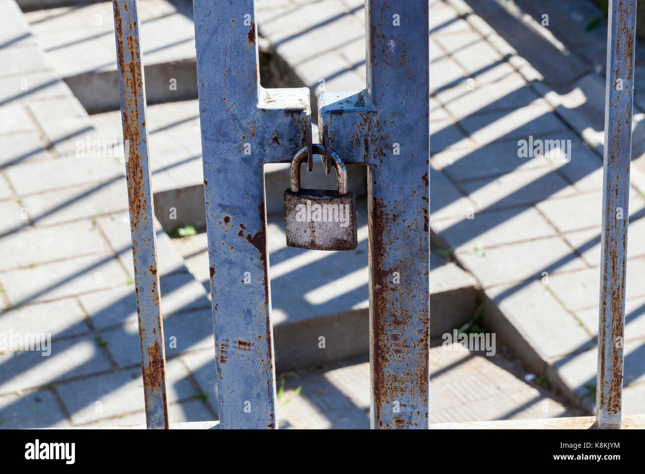 Rust-covered metal padlock, closed on a metal grill at the gate. photo ...