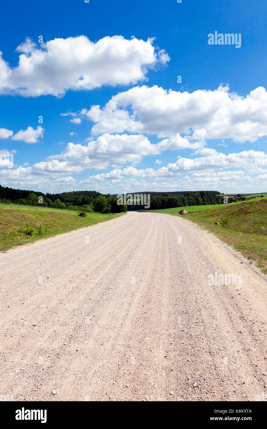 A wide country road against a blue sky with clouds. On the sides of the ...