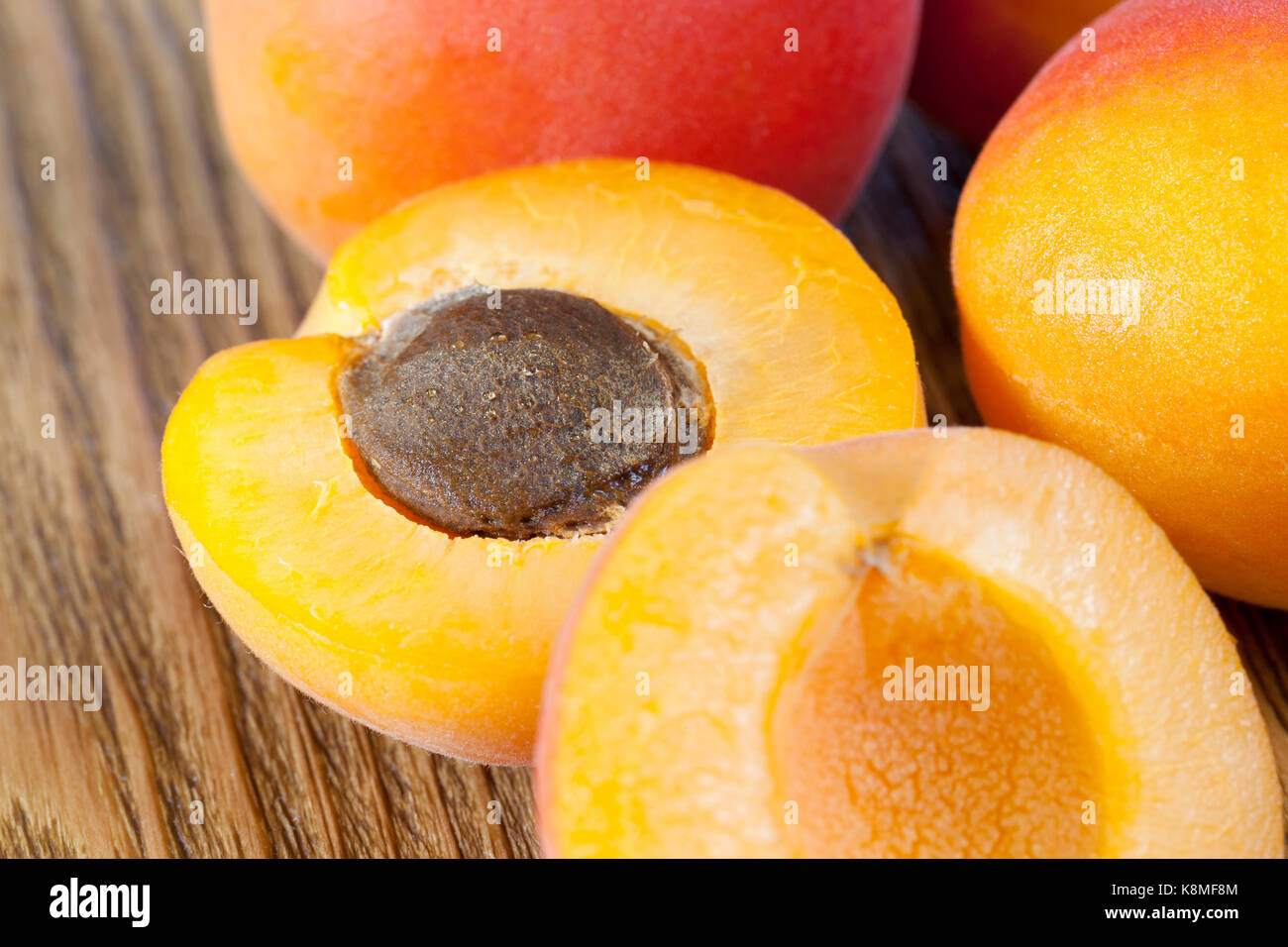 a bunch of apricots lying on an old wooden table. one apricot is ...