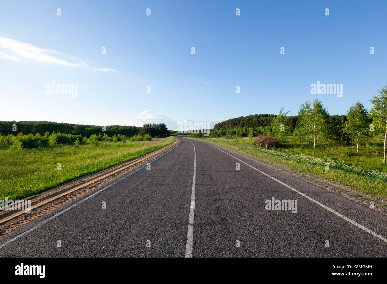 A small road in the summer. The roadway is divided by a white line of ...