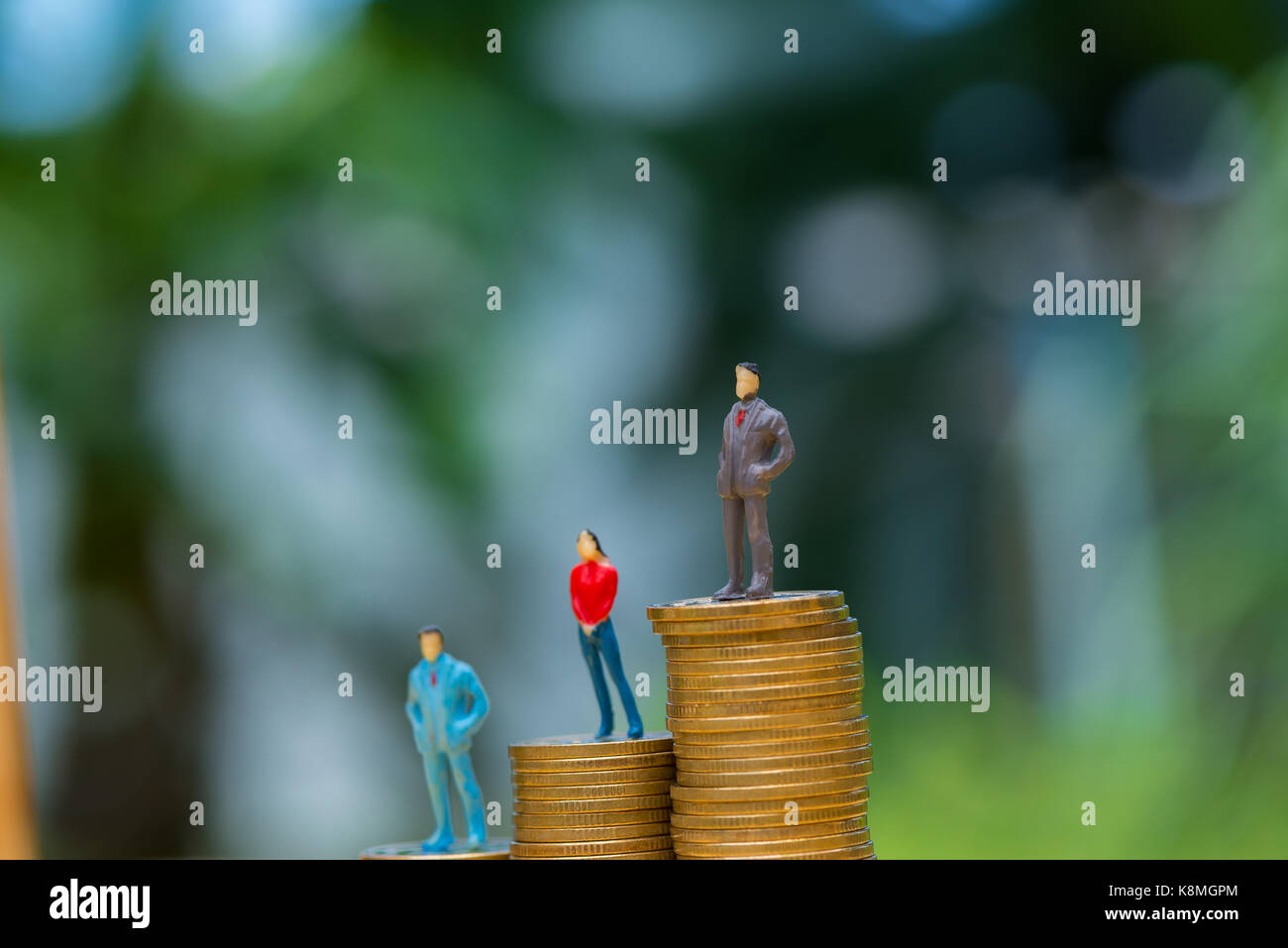 Miniature people, small figures businessmen and woman on top of coins ...