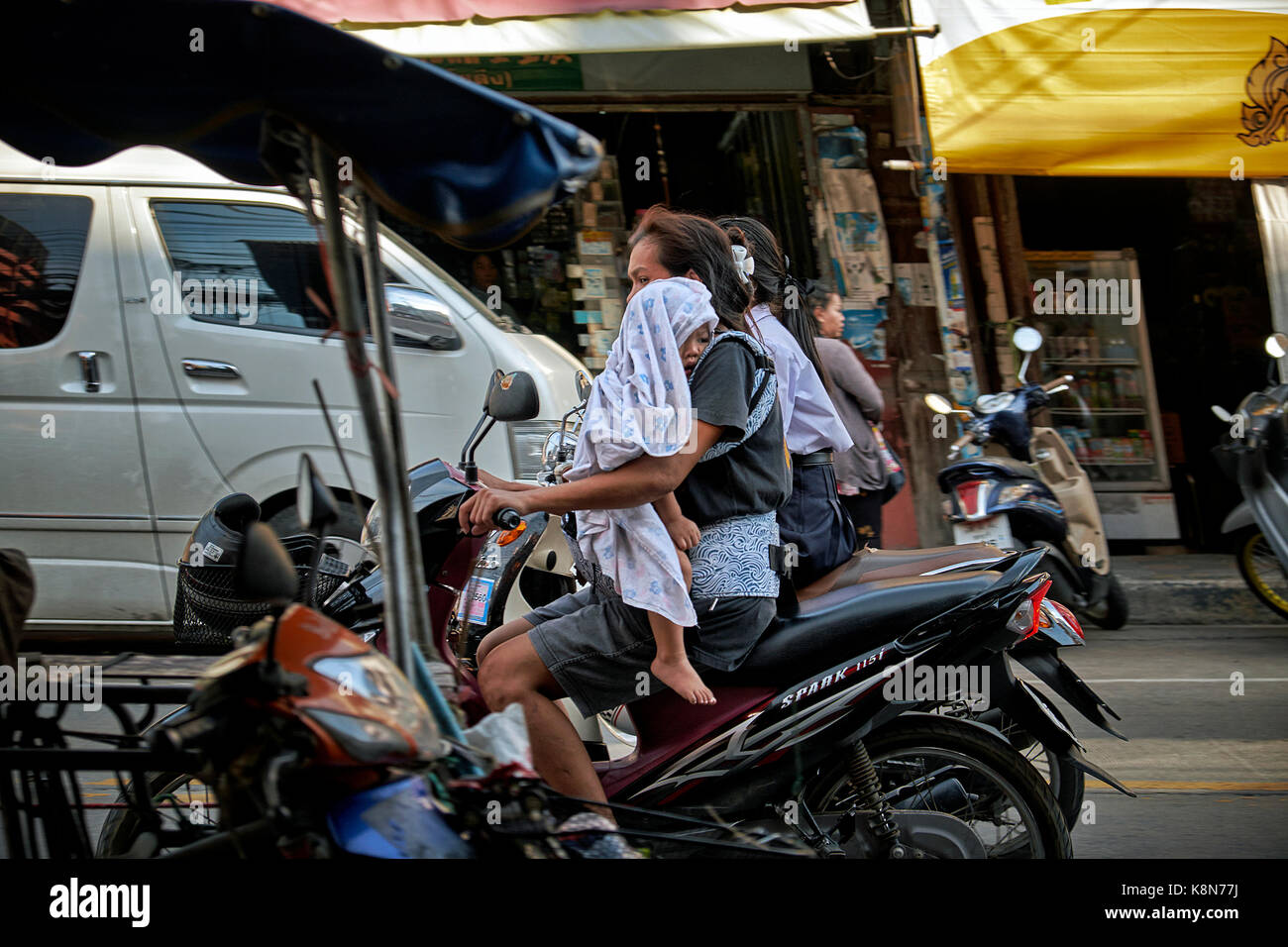Woman carrying a child in her arms whilst riding a motorcycle. Thailand ...