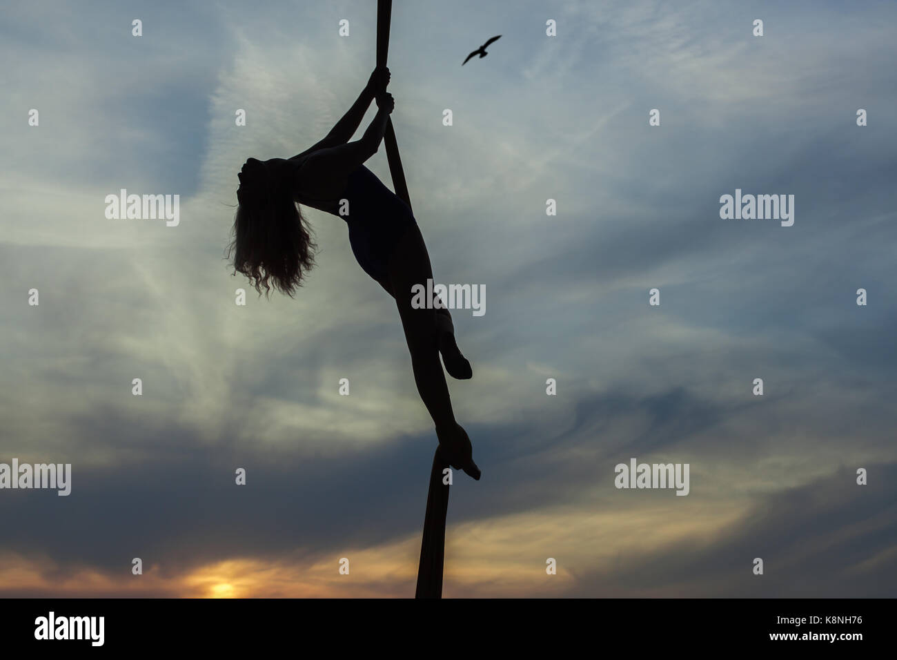 Woman aerial acrobat dances in the air against the sky, she ...