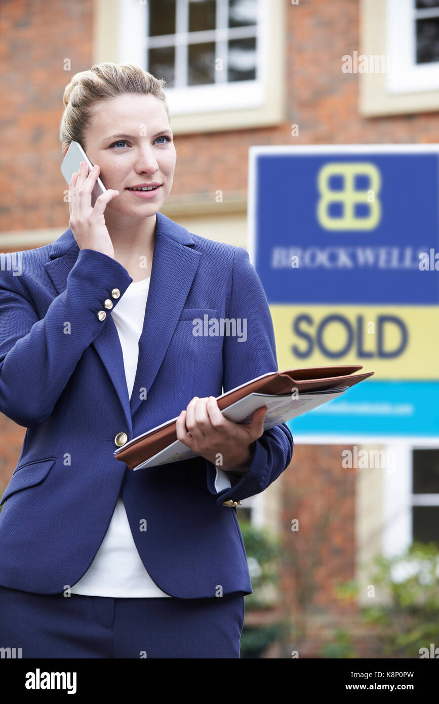 Female Realtor On Phone Outside Residential Property For Sale Stock ...