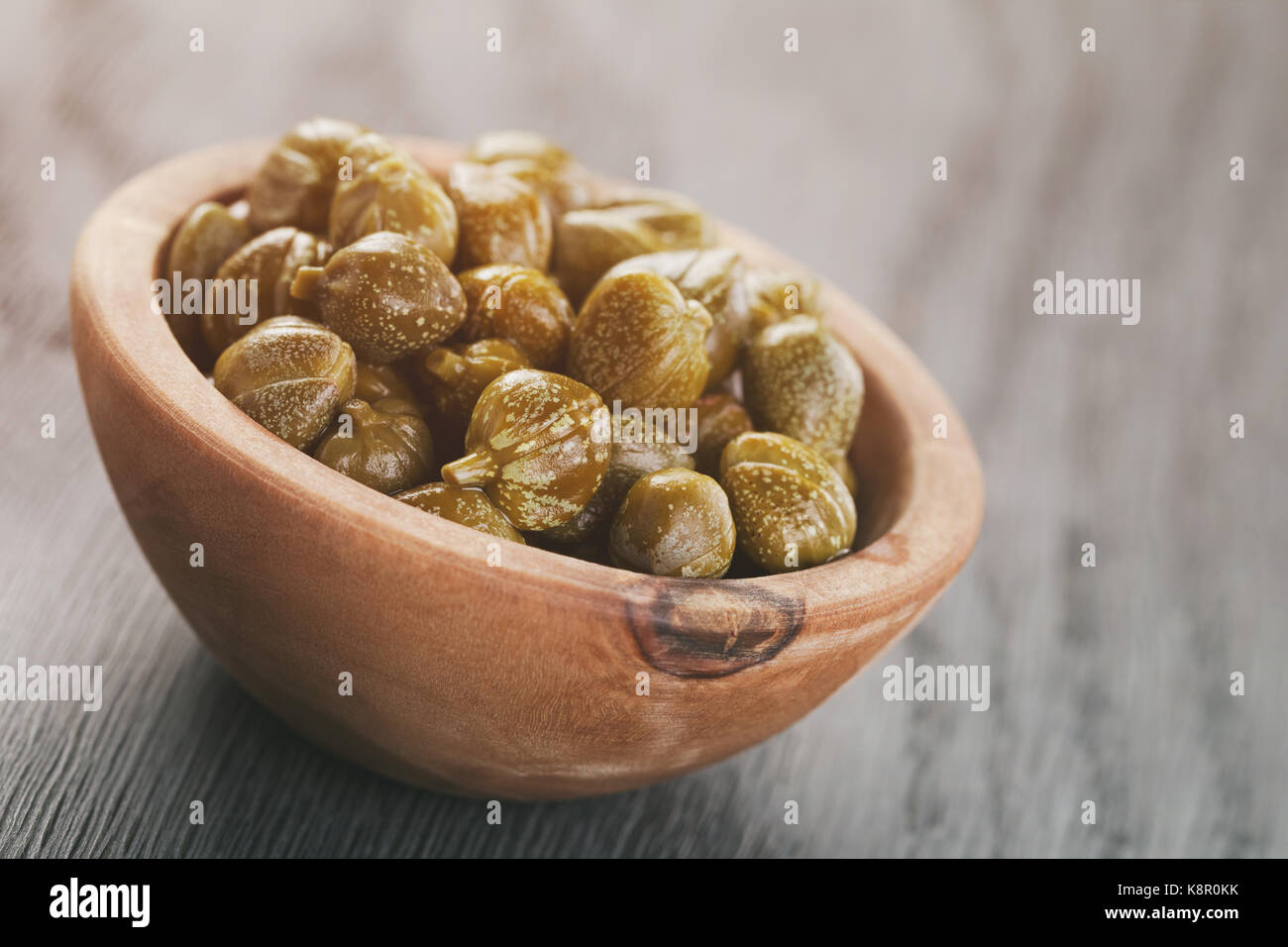marinated capers in olive bowl on wood table Stock Photo - Alamy
