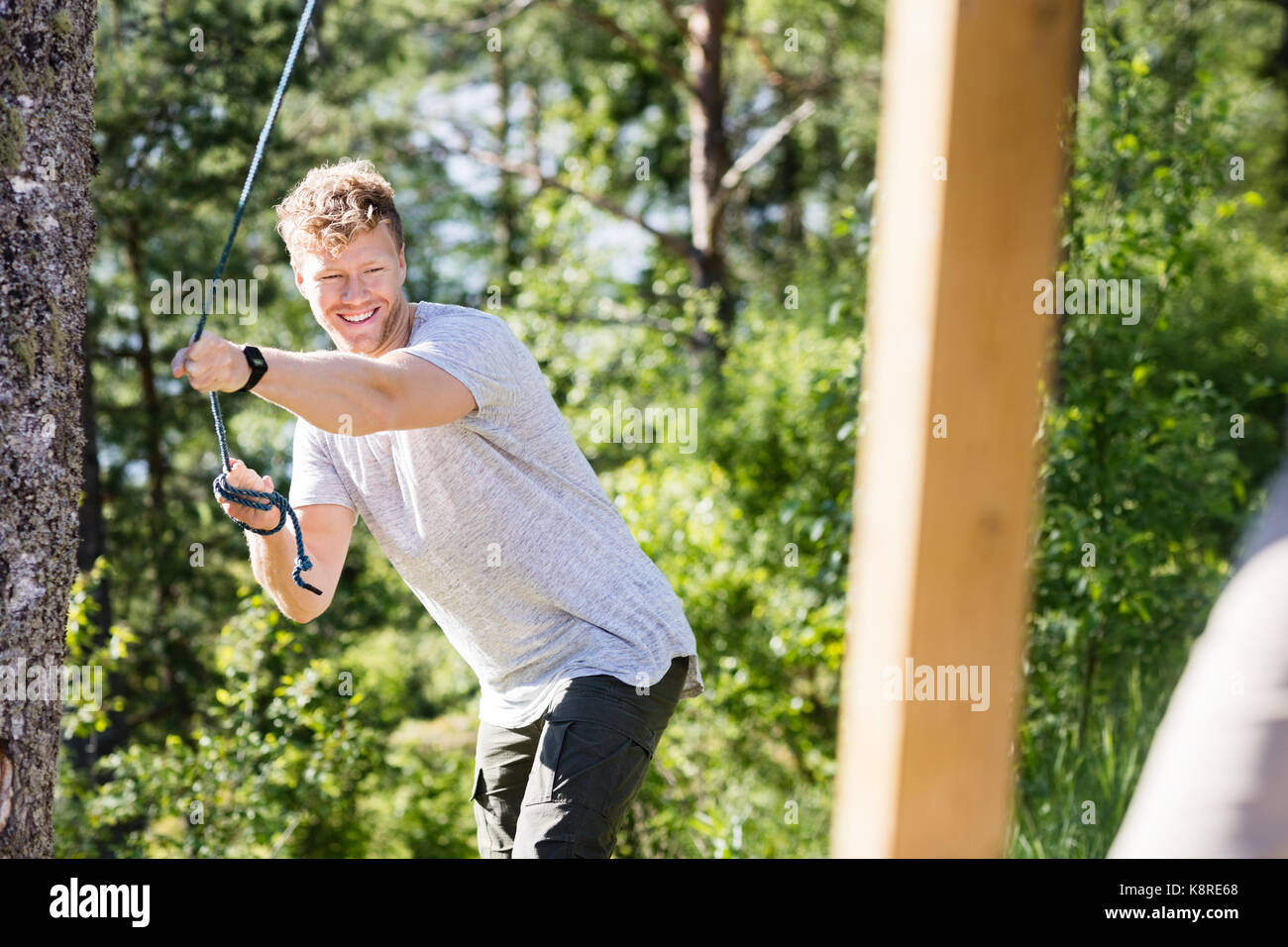 Happy Man Pulling Rope Attached To Wooden Structure In Forest Stock ...