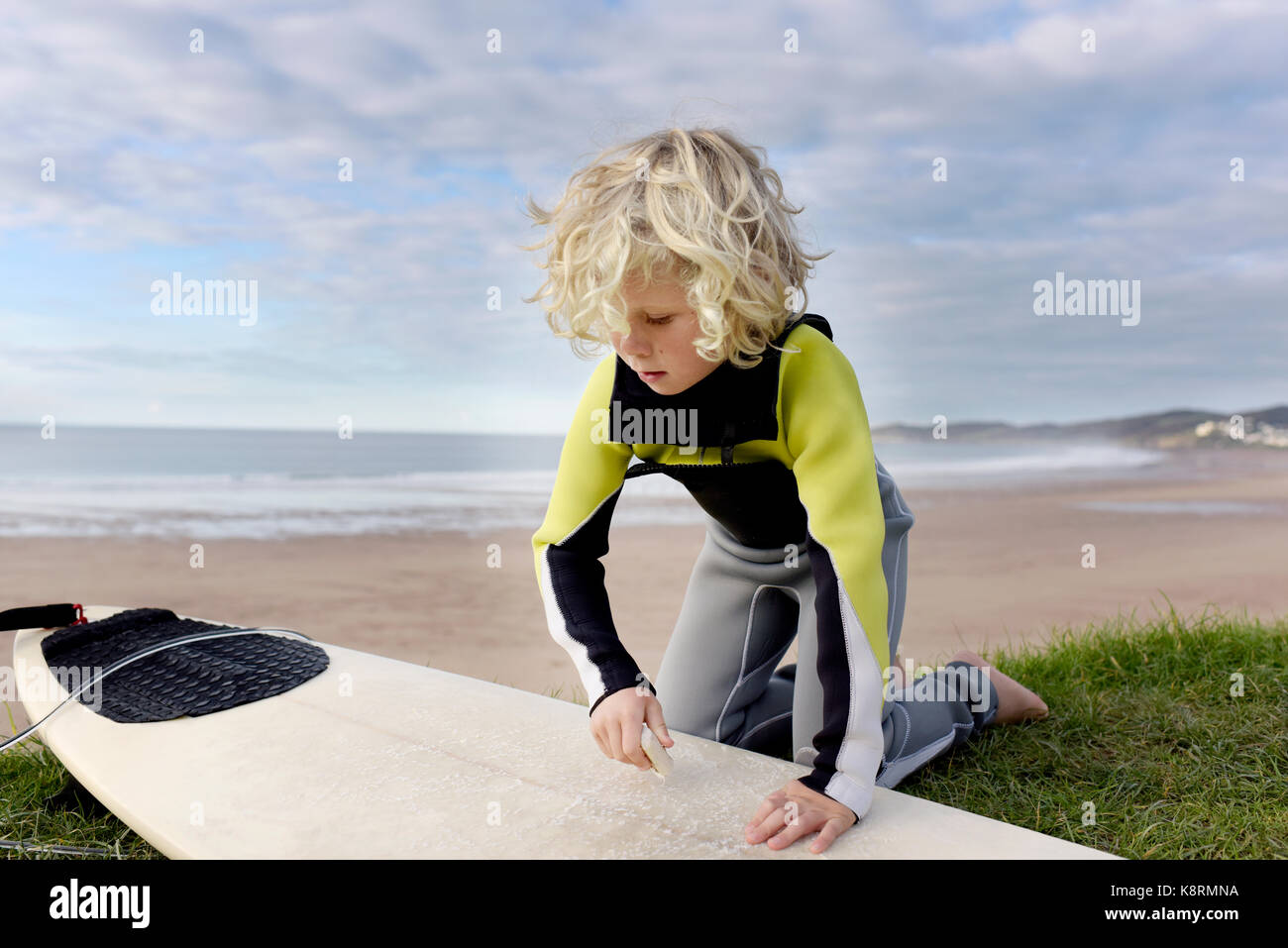 Young boy getting ready to surf with his surfboard on the beach wearing ...