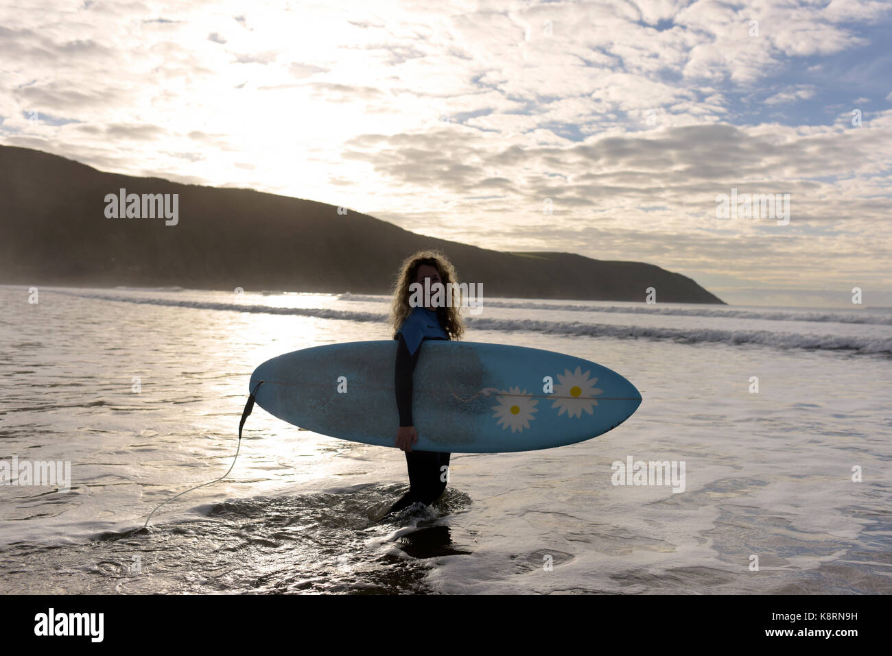 A woman getting ready to surf carrying her surfboard on the beach ...