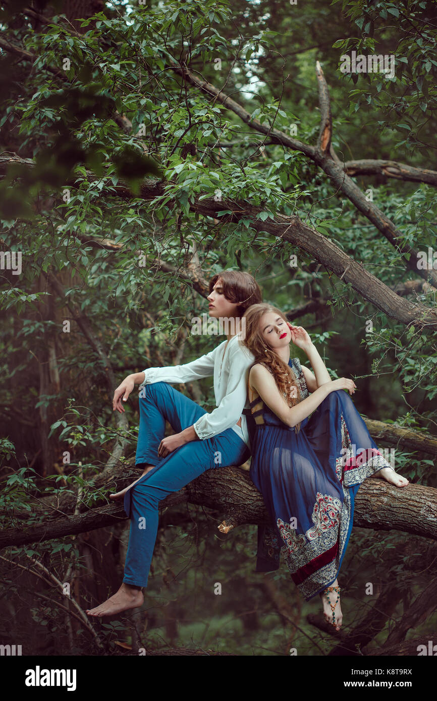 Young couple of elves in love siting on branch in magical forest ...
