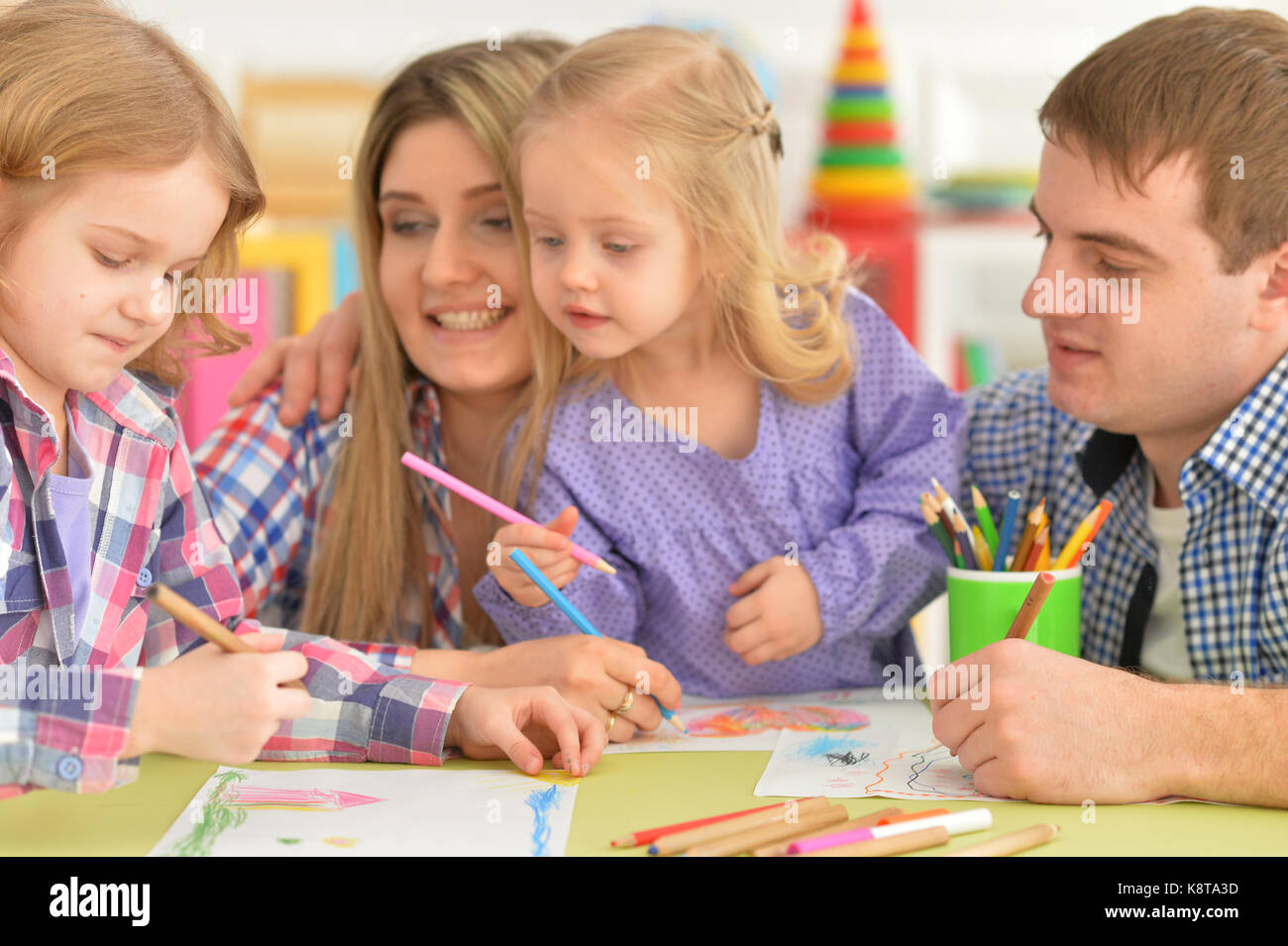 parents with adorable little daughters sitting at table and drawing ...