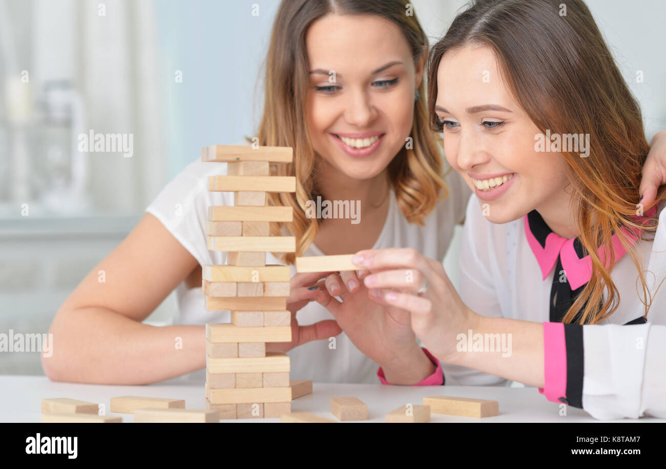 Two emotional sisters sitting at table and playing with wooden blocks ...