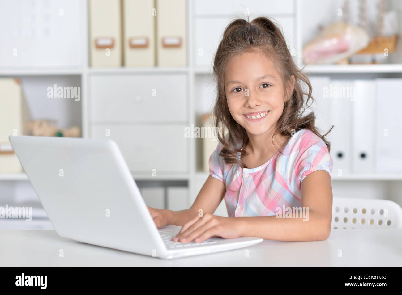 Little girl sitting at table and using modern laptop Stock Photo - Alamy