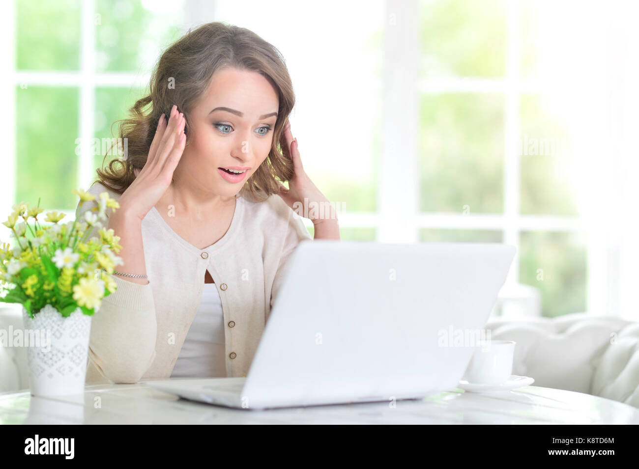 surprised Beautiful young surprised woman sitting at table and using ...