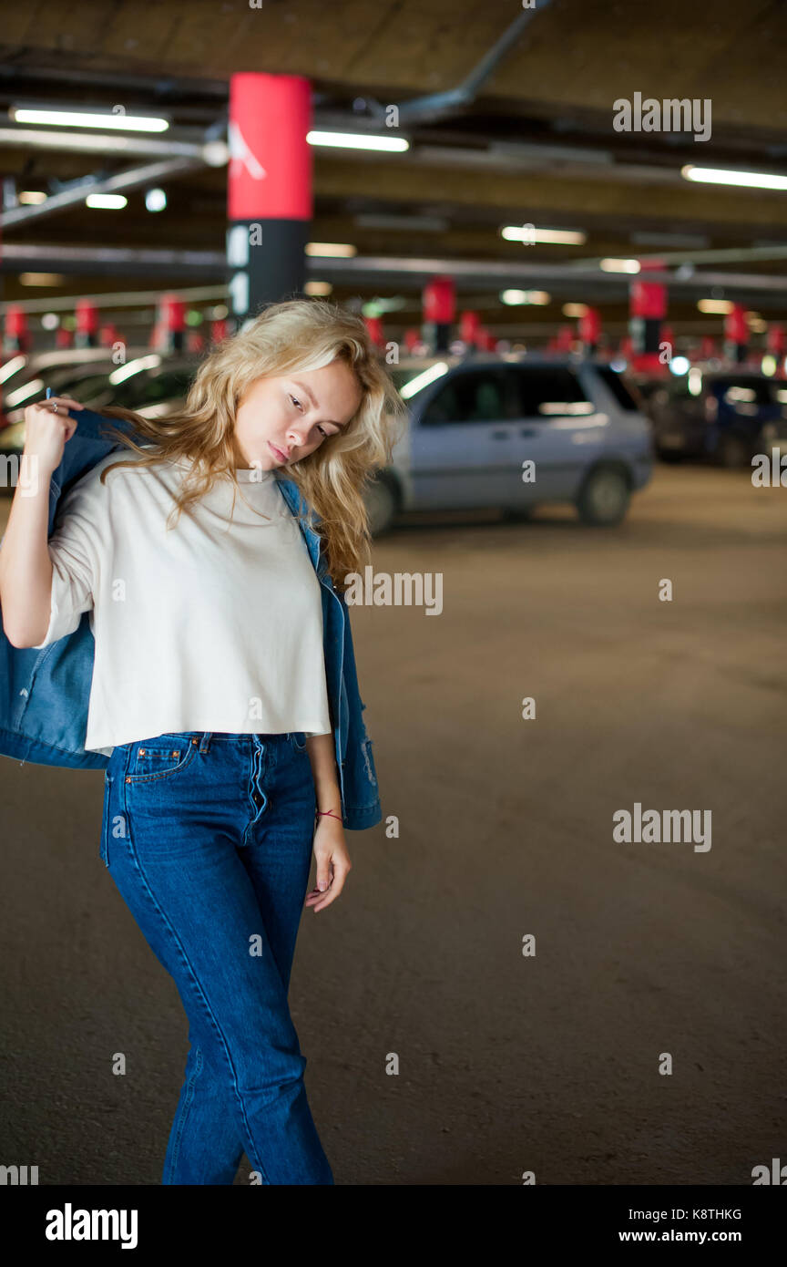 young beautiful woman in jeans clothes in parking of shopping center ...