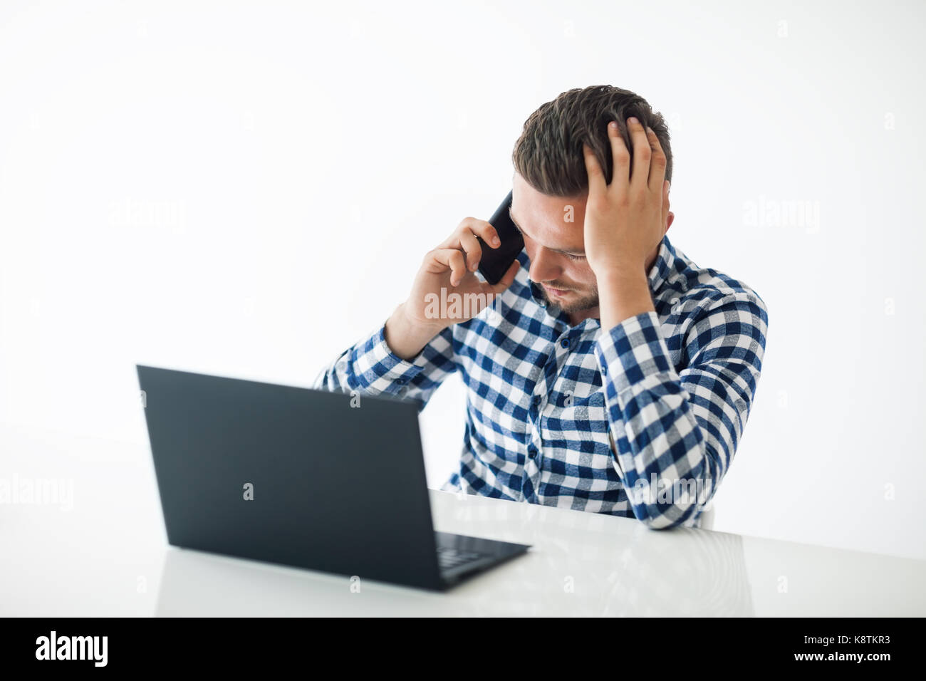 Stressful tired young businessman with laptop speaking on mobile phone ...