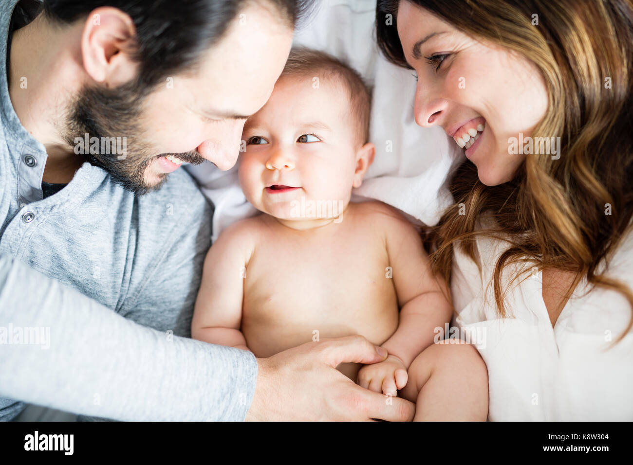 Mother father and baby child on a white bed Stock Photo - Alamy