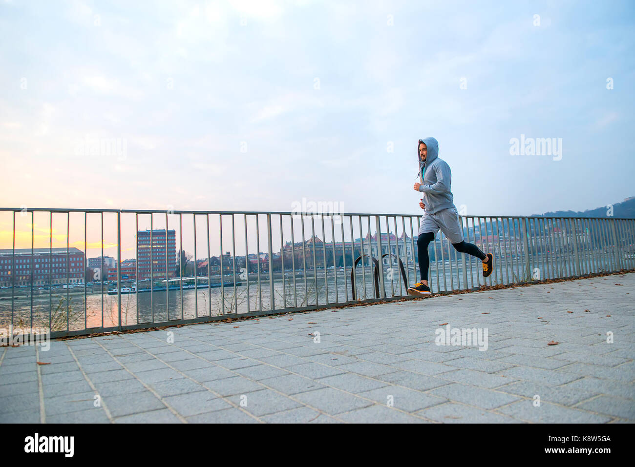 A handsome young man running in the sunset next to a fence on the ...