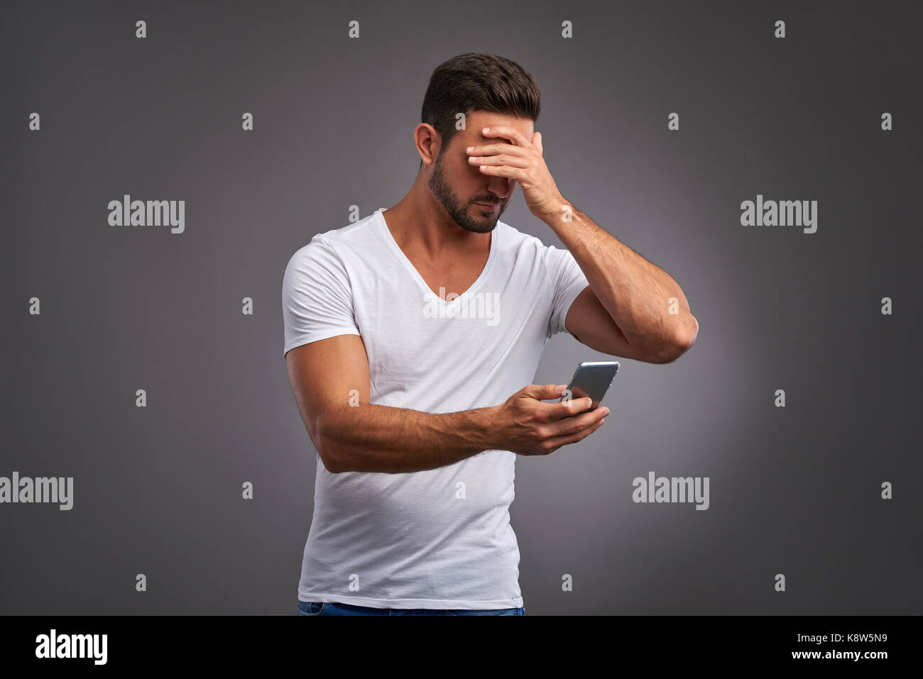 A handsome young man looking at a smartphone and feeling frustrated and ...
