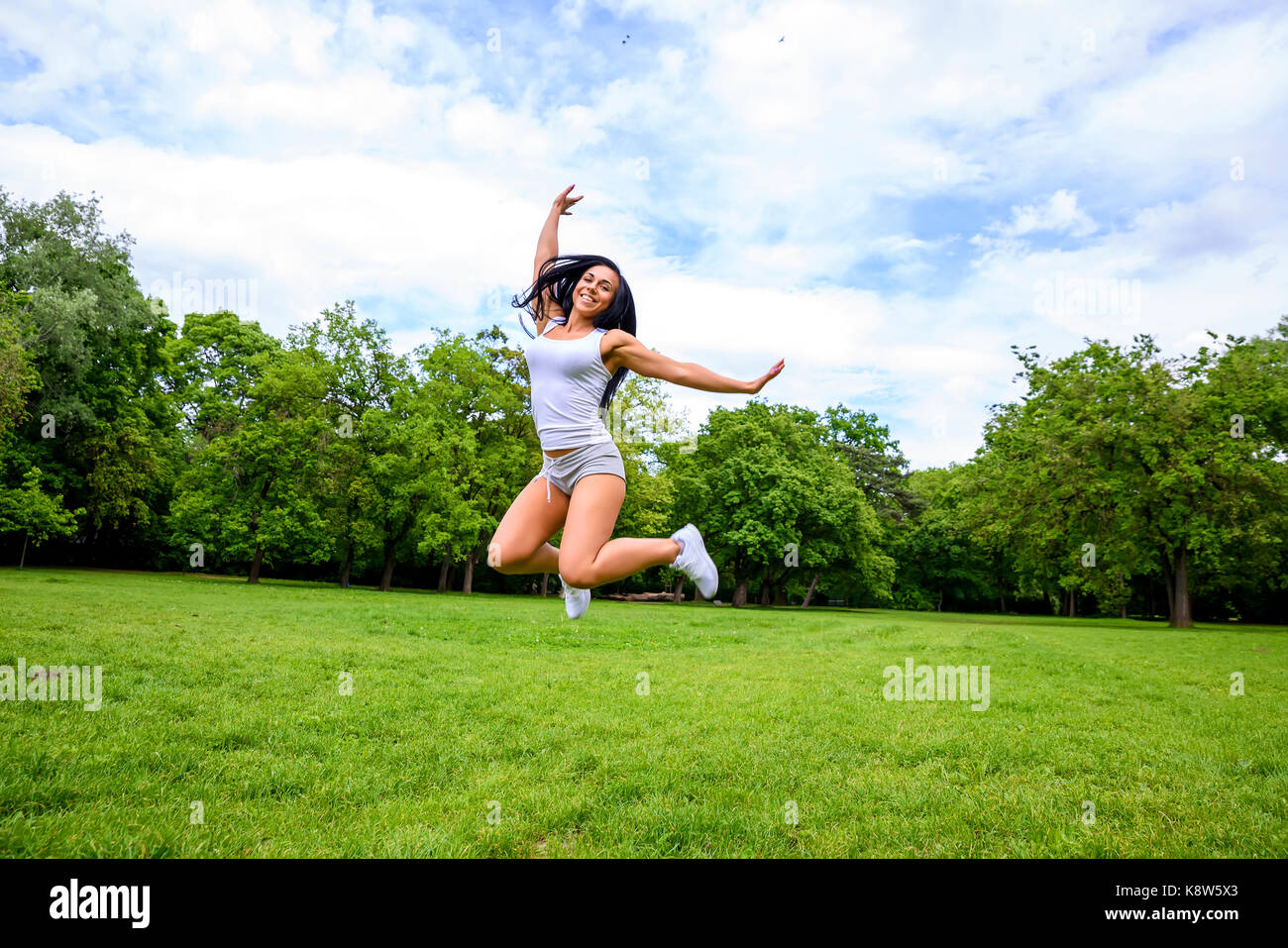 A beautiful young sporty girl jumping on a field in a park while ...