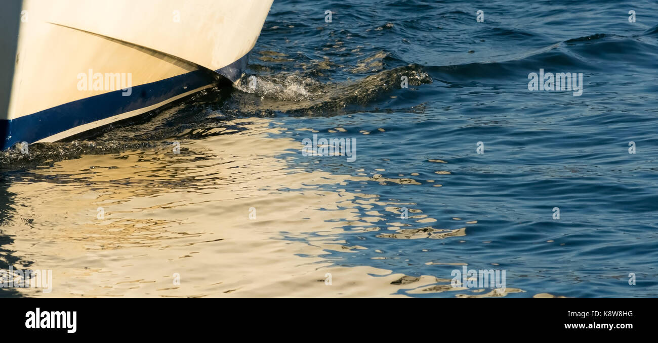 A small wave shows how the white hull of a small boat cuts through ...