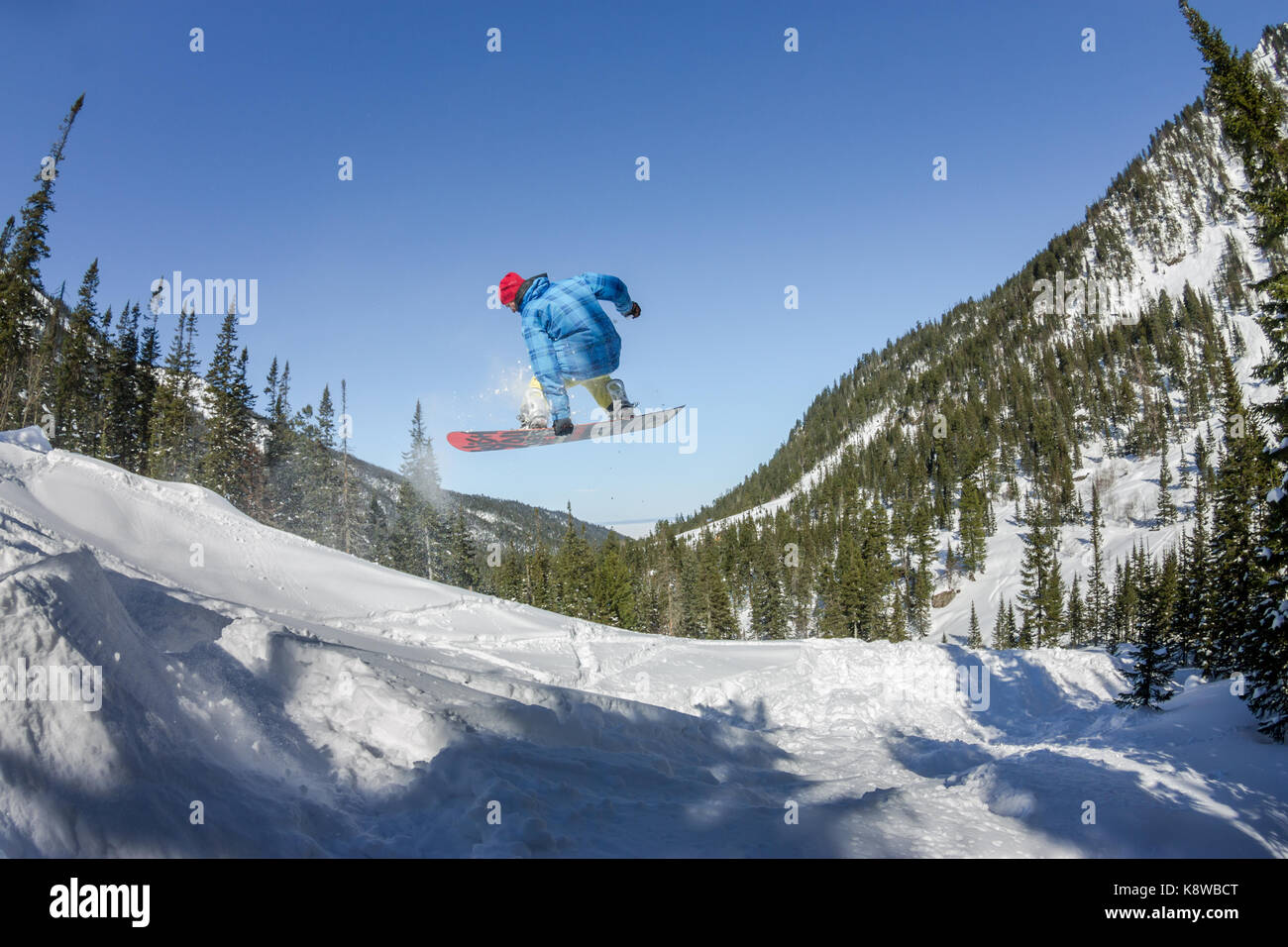 Snowboarder freerider jumping from a snow ramp in the sun on a ...