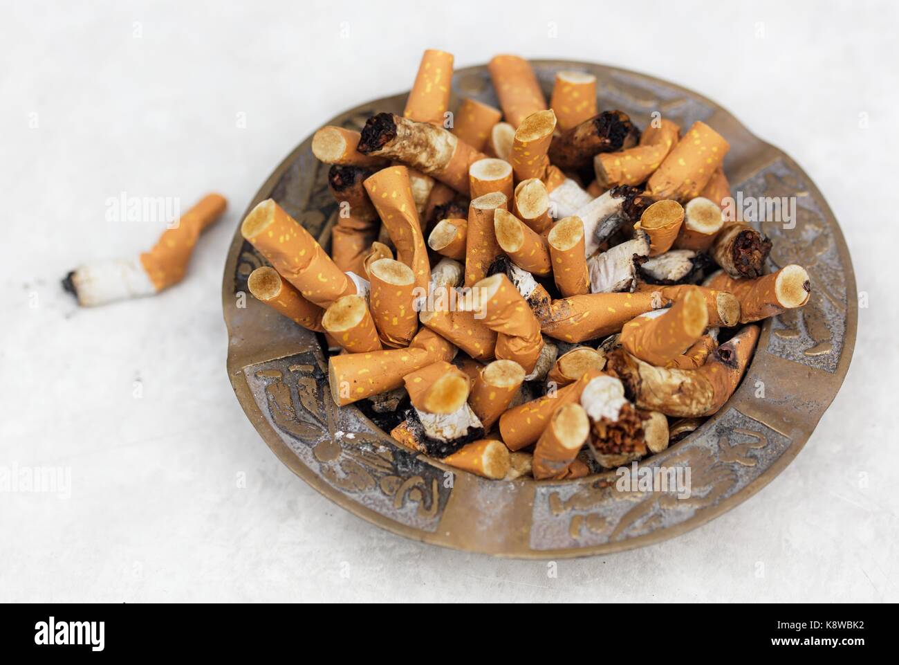 Messy full ashtray on white table Stock Photo - Alamy