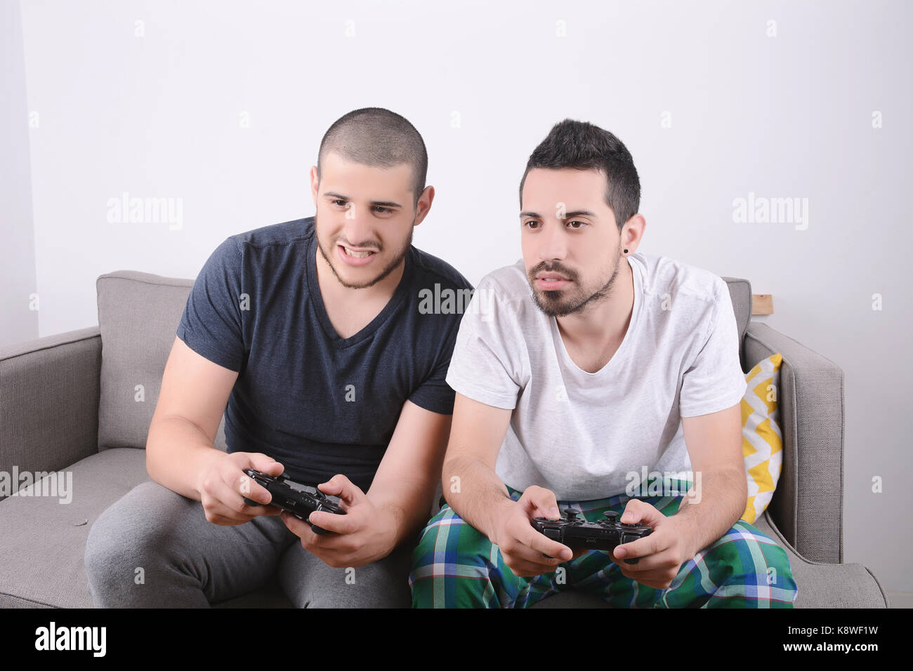 Portrait of two friends playing videogames and sitting on couch ...
