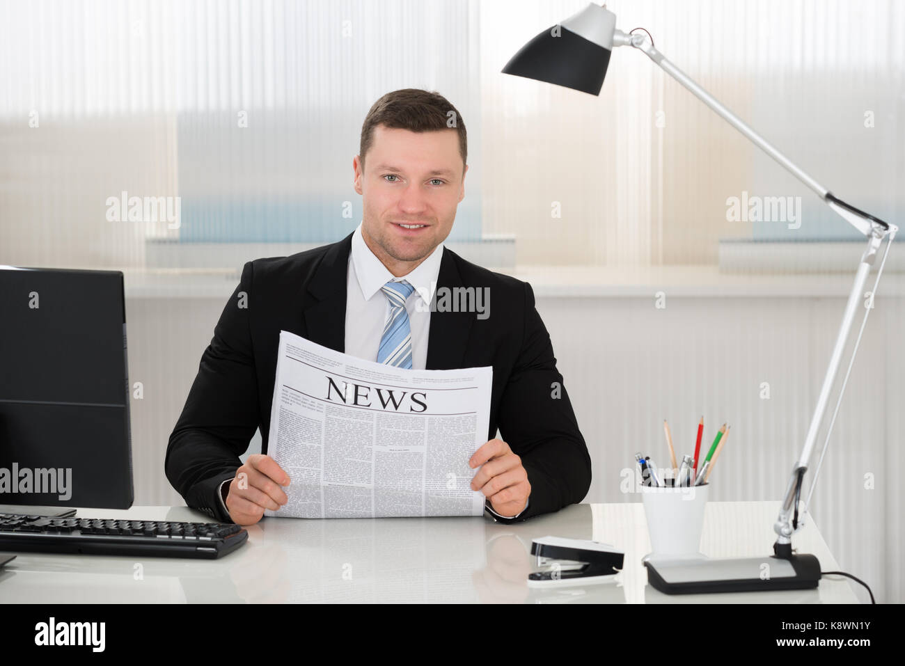 Portrait of smiling businessman holding newspaper while sitting at ...