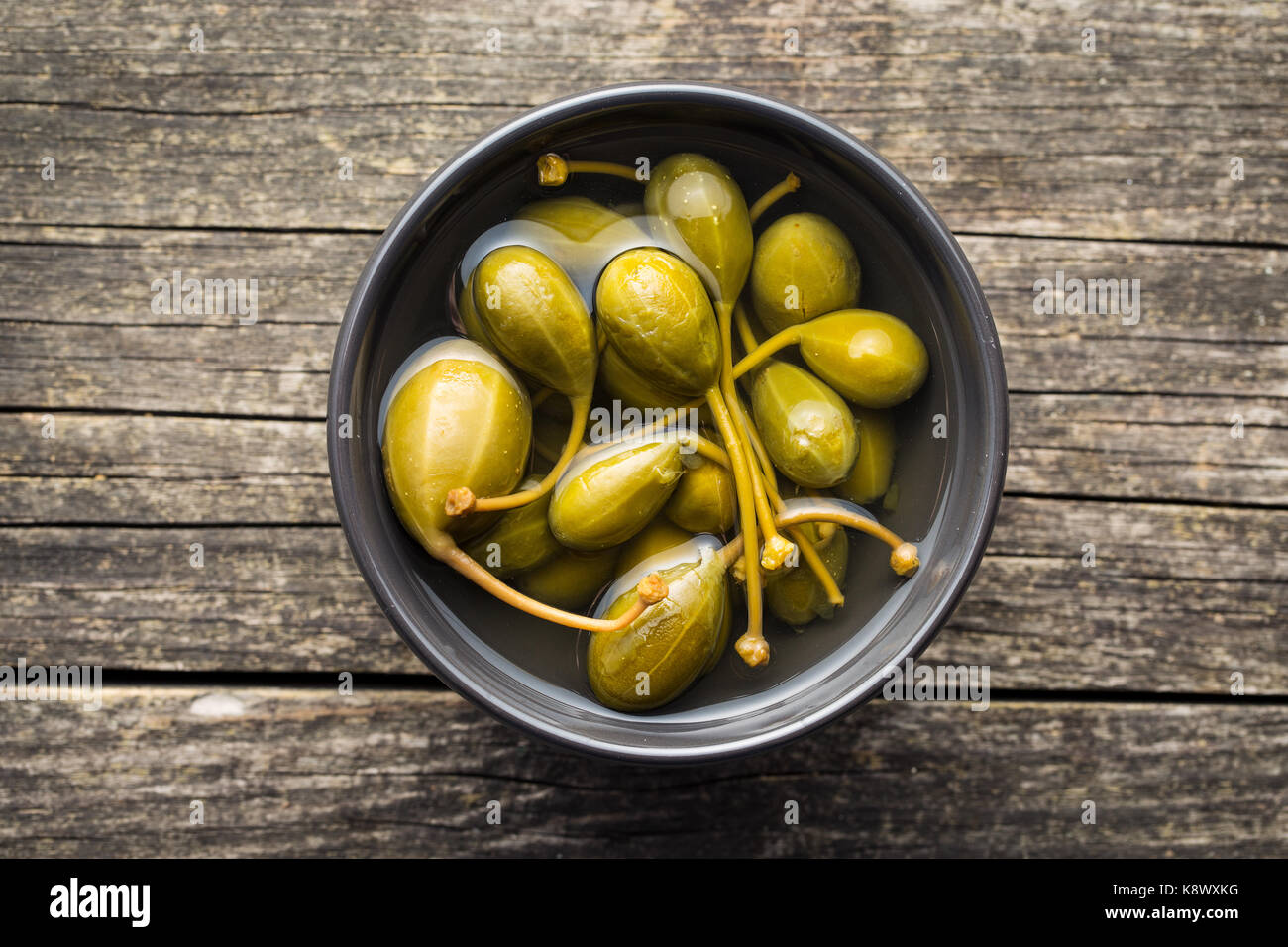 Pickled caper berries in bowl on old wooden table Stock Photo - Alamy