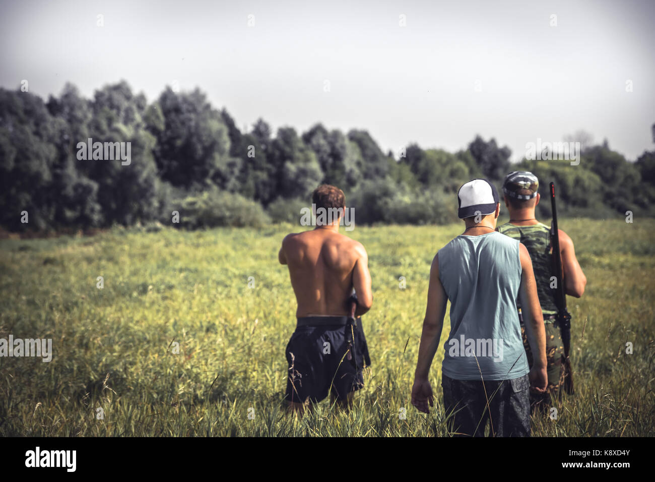 Group of strong male hunters going through rural field with tall grass ...
