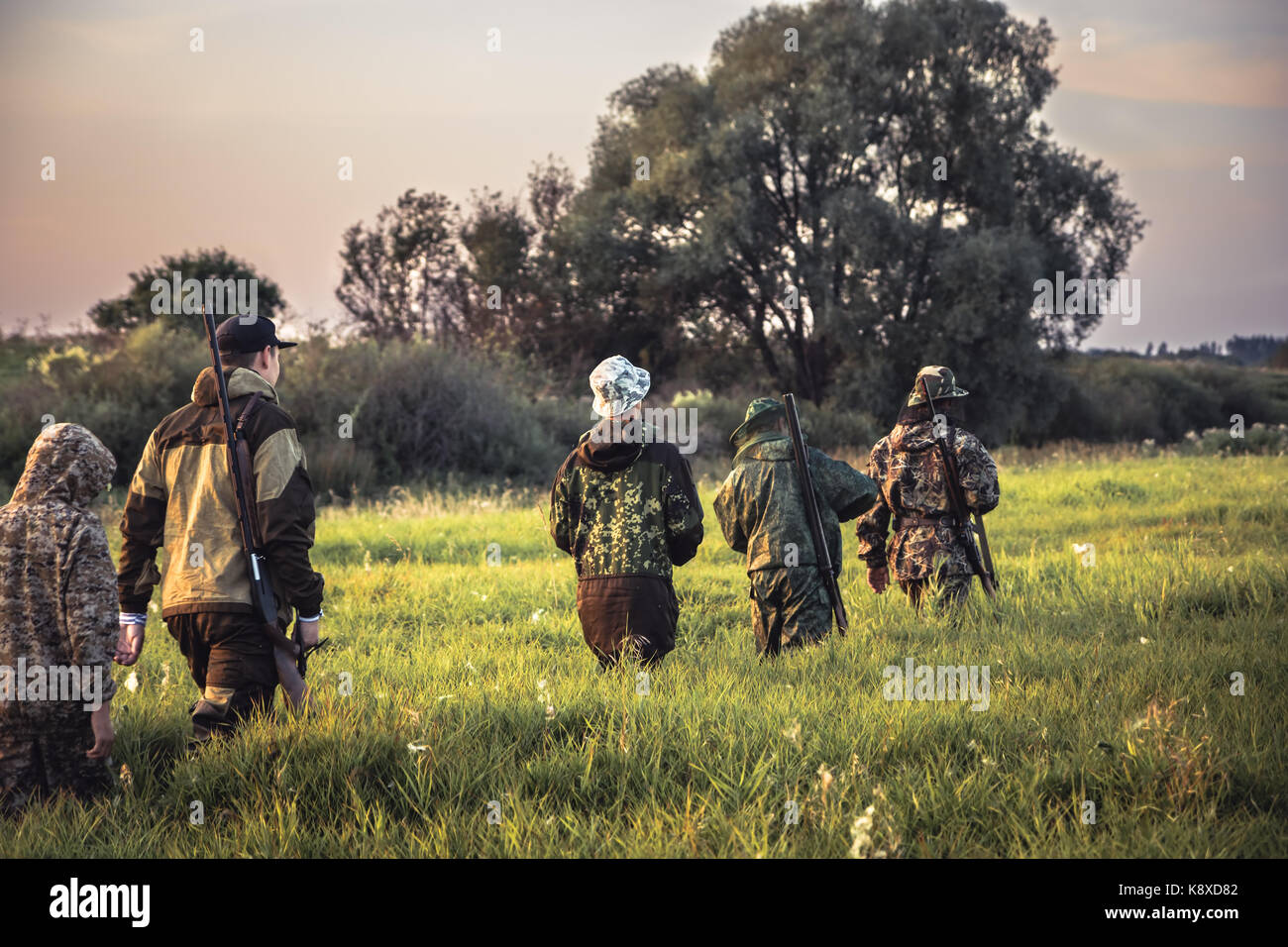 Group of men hunters going through tall grass on rural field at sunset ...