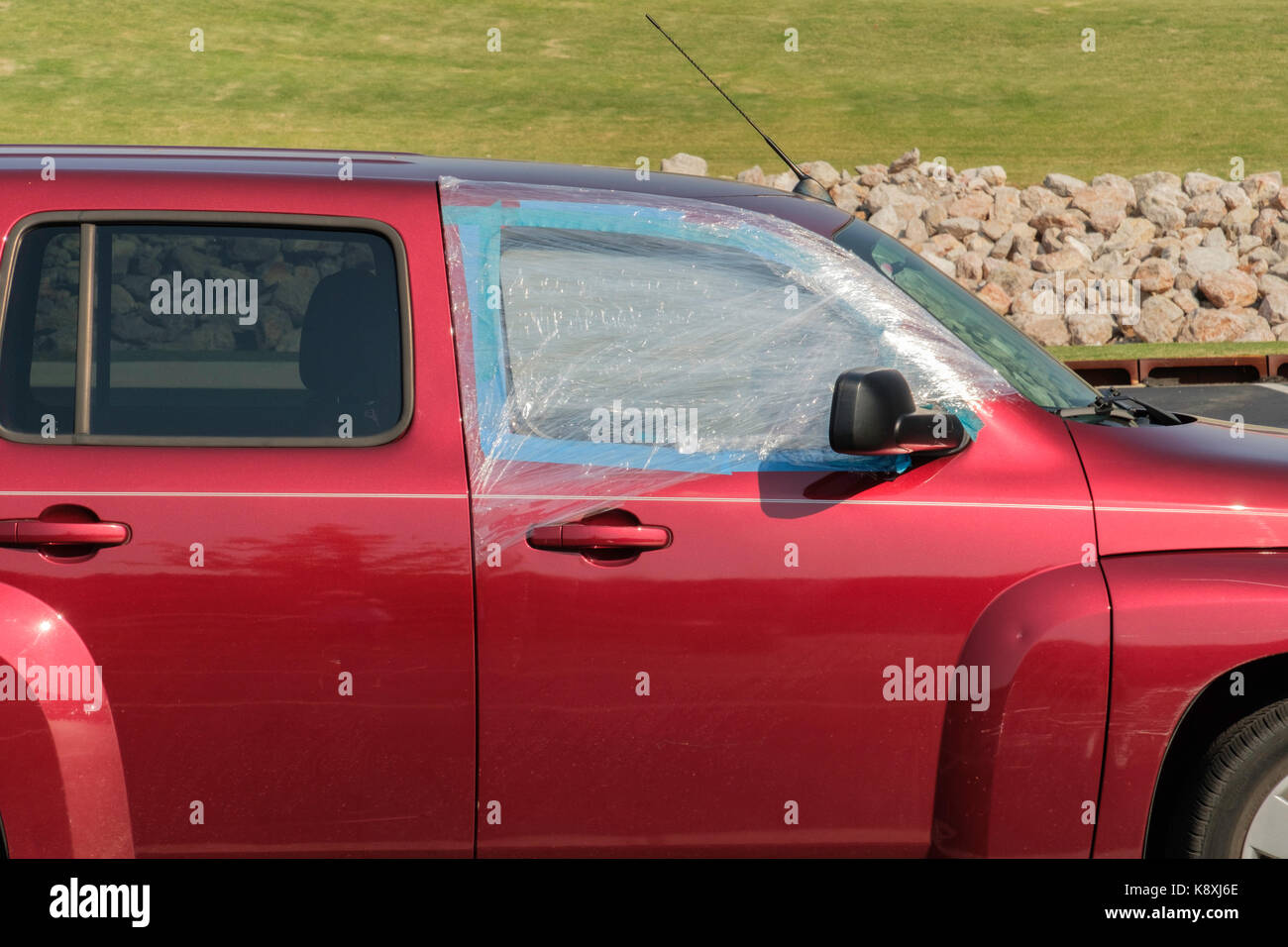 A red automobile with a broken passenger window, taped up with plastic ...