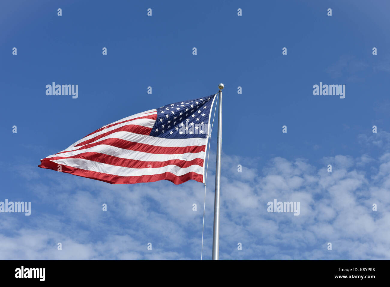 Large American Flag flapping in the wind with small cloud puffs below ...