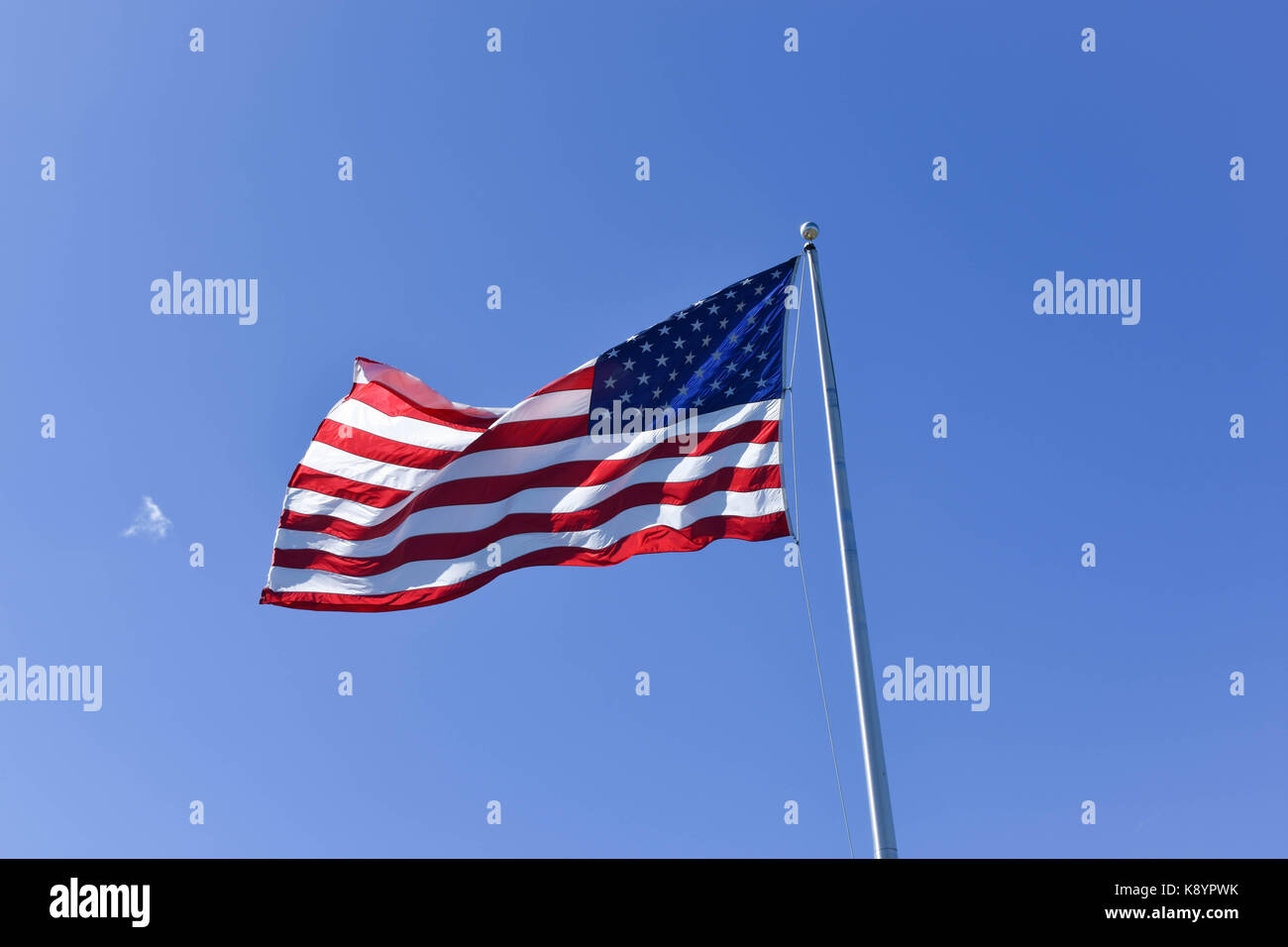 Sun highlights through American Flag with light blue sky background ...