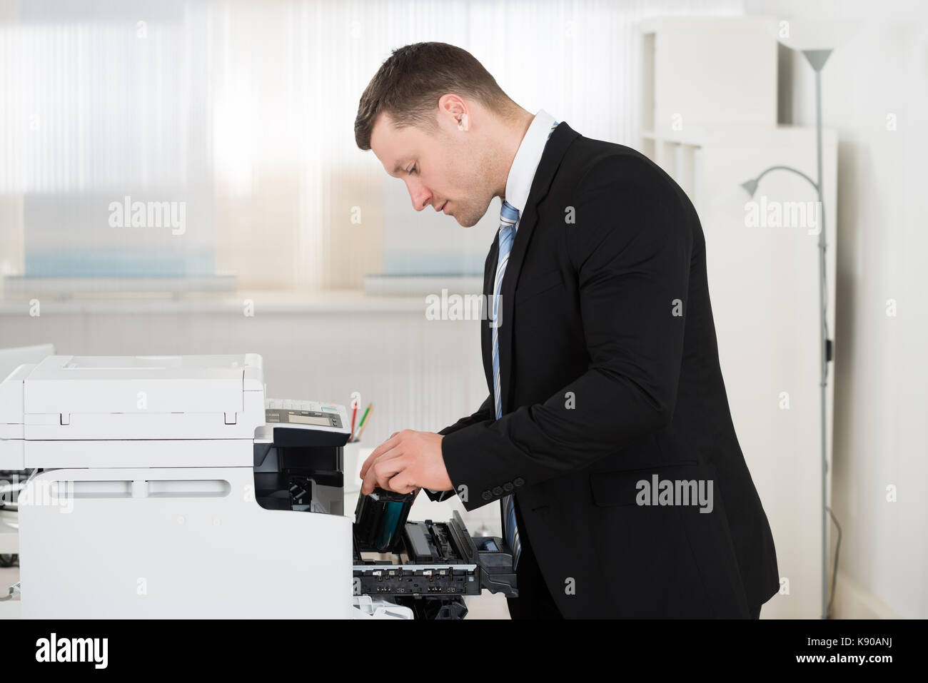 Side view of businessman adjusting cartridge in photocopy machine at ...