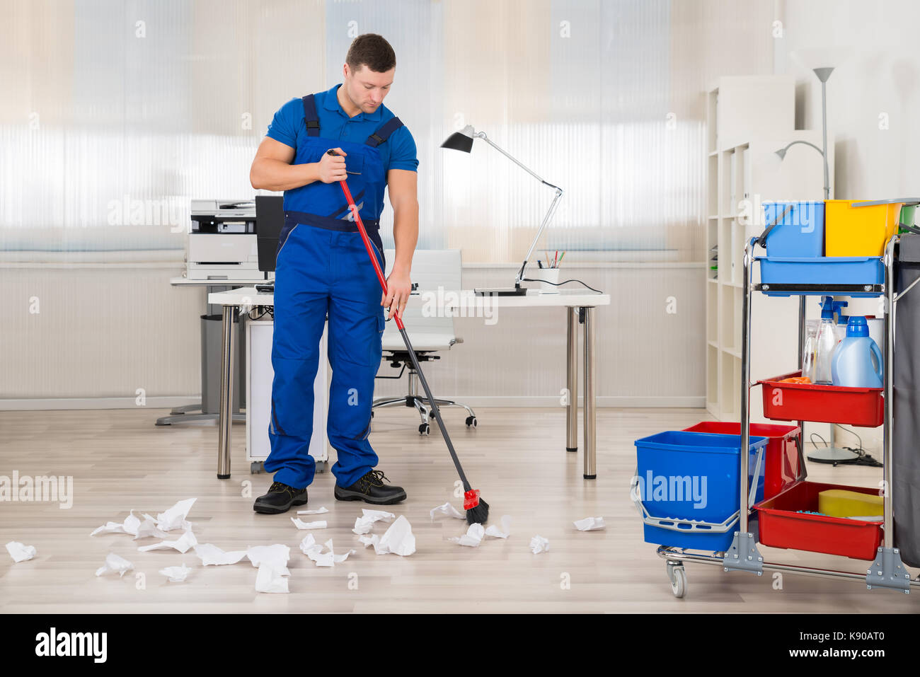 Full length of male janitor cleaning floor with broom in office Stock ...