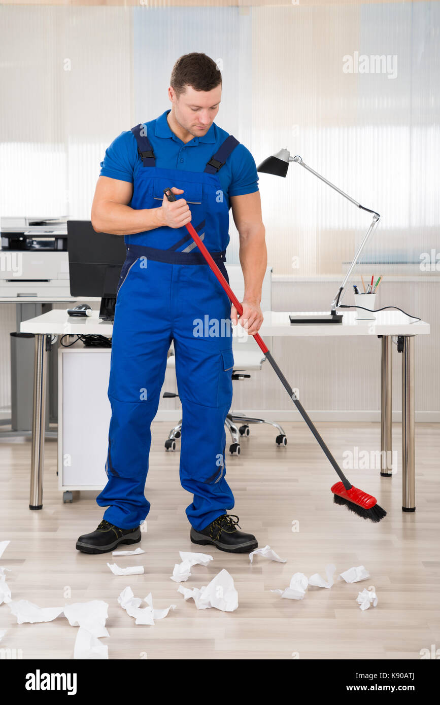 Full length portrait of smiling janitor holding broom while standing in ...