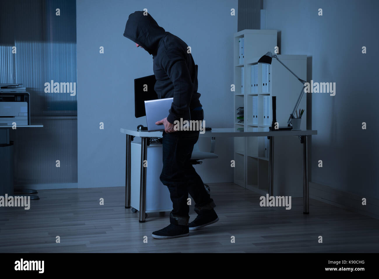 Full length side view of robber stealing laptop from office at night ...