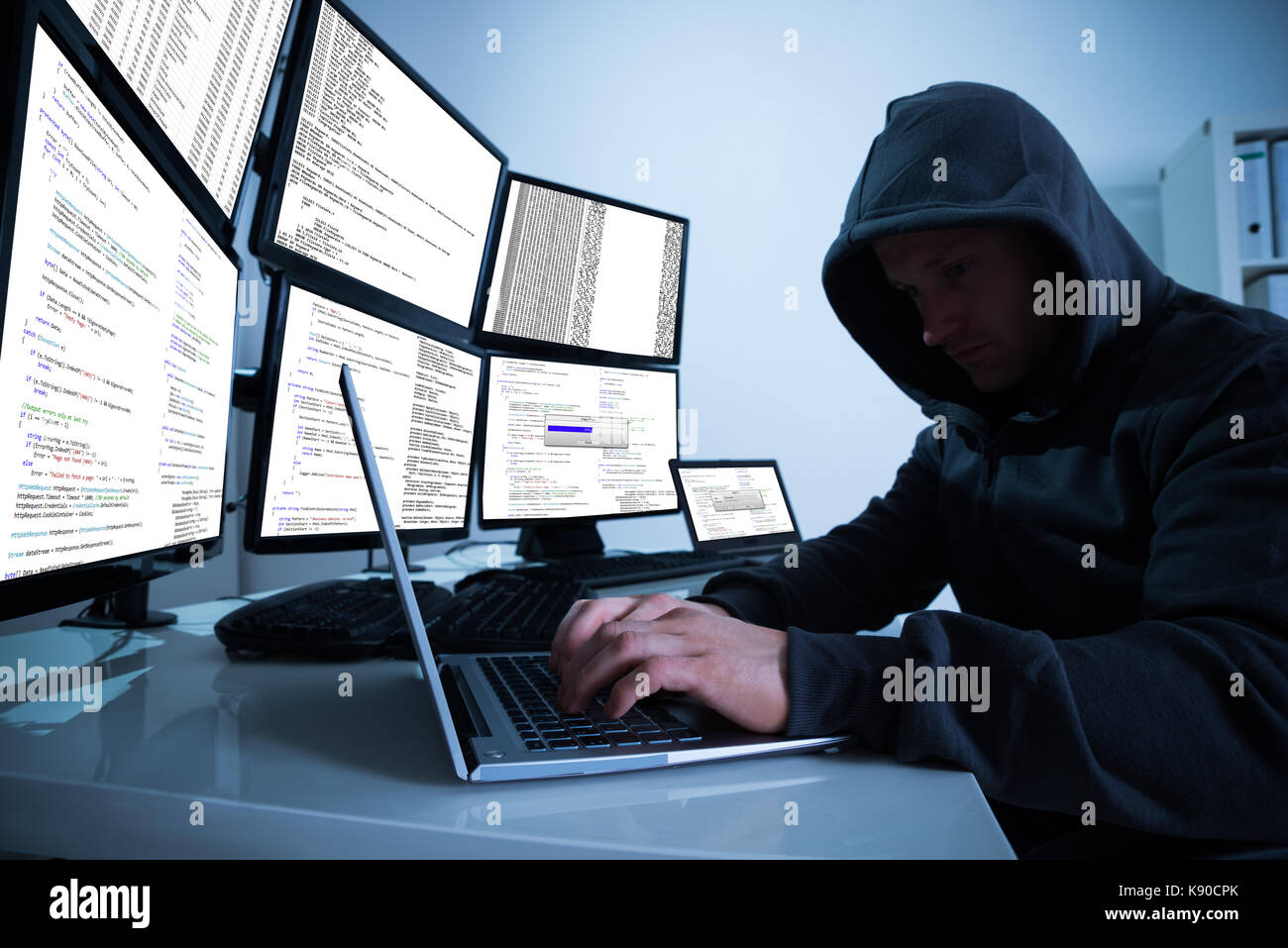 Hacking laptop against multiple monitors at desk Stock Photo - Alamy