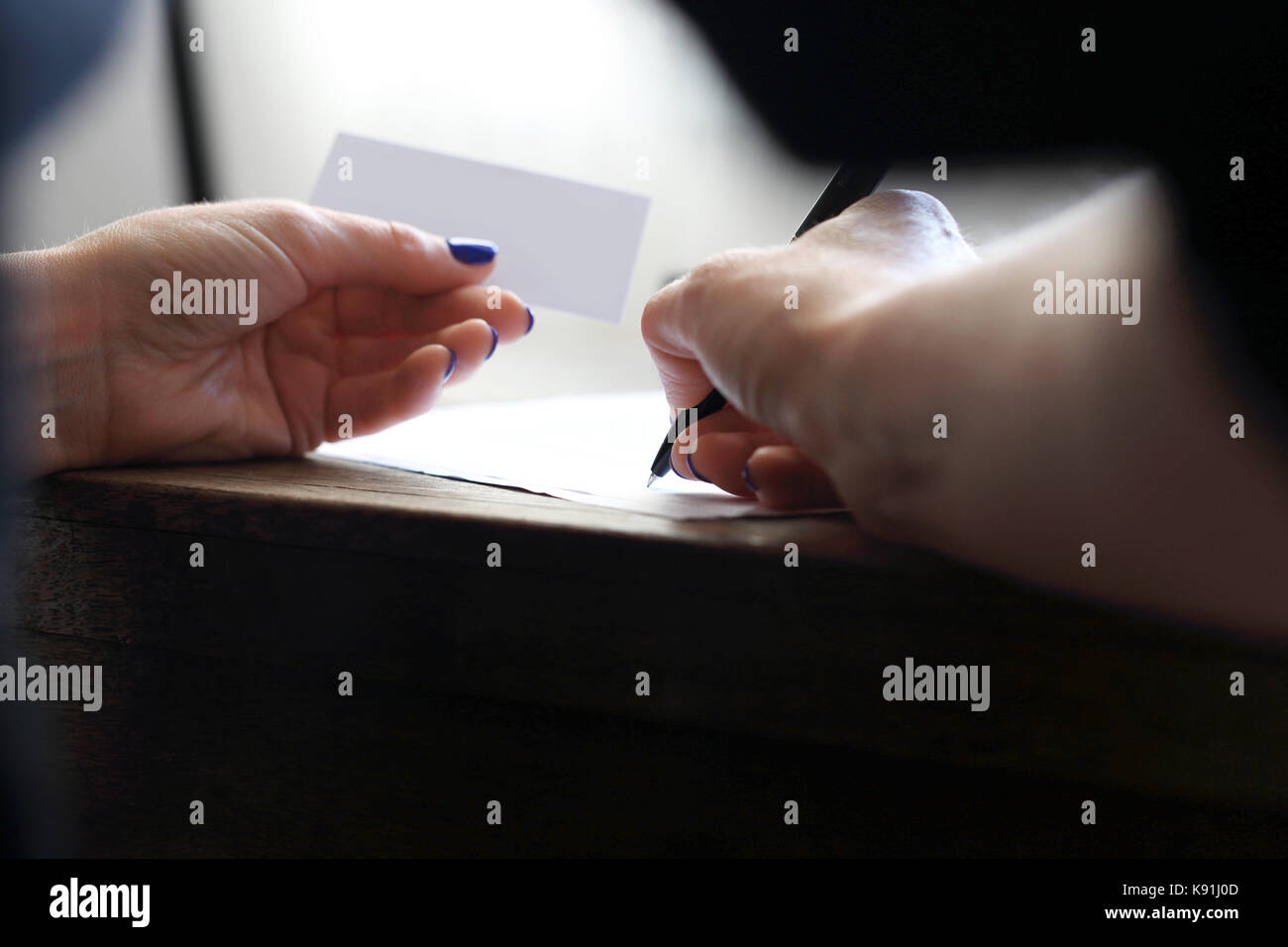 Signing the contract. Woman signs a document holding a business card in ...