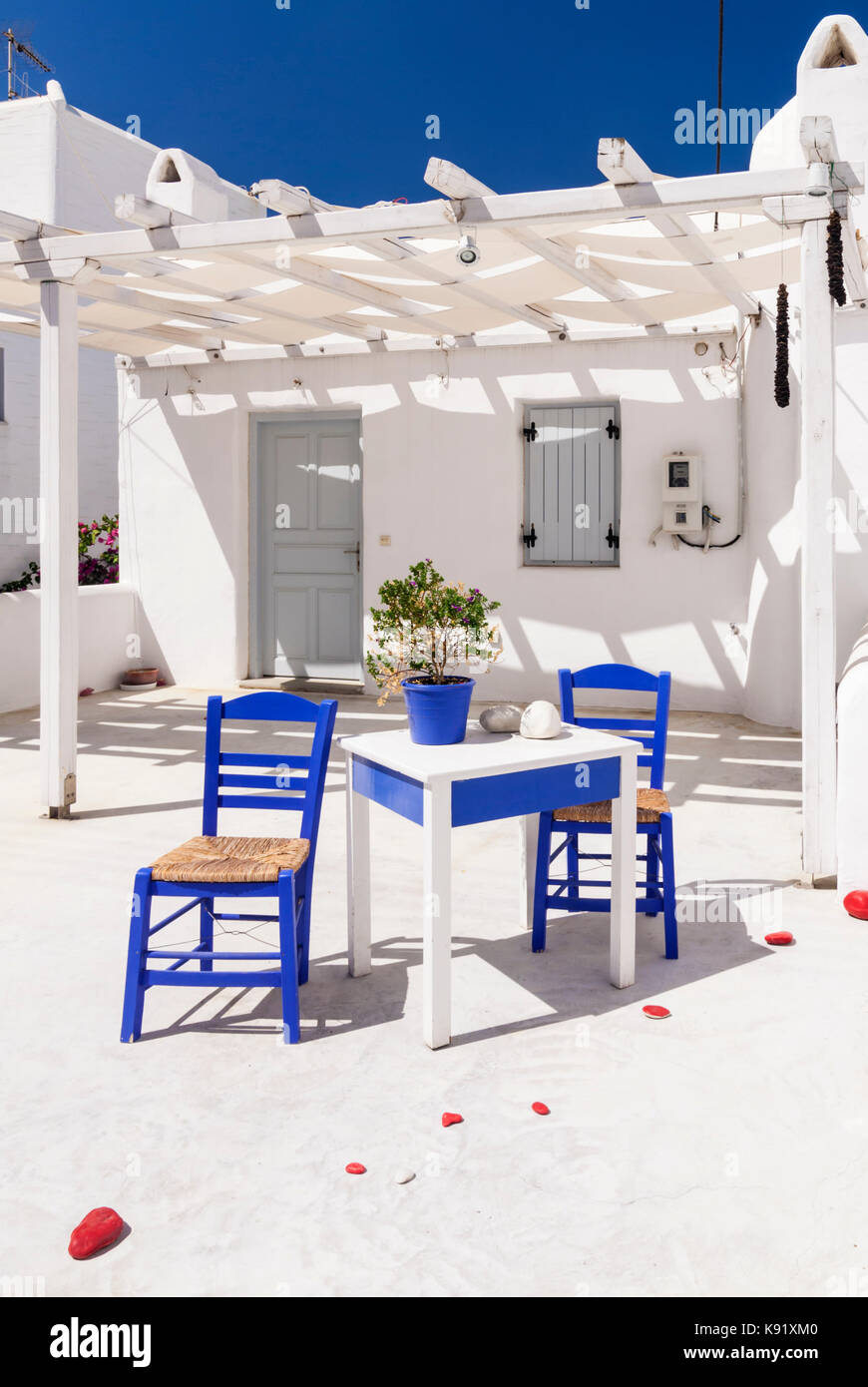 Pretty Greek Island scene of a whitewashed house with blue chairs and ...
