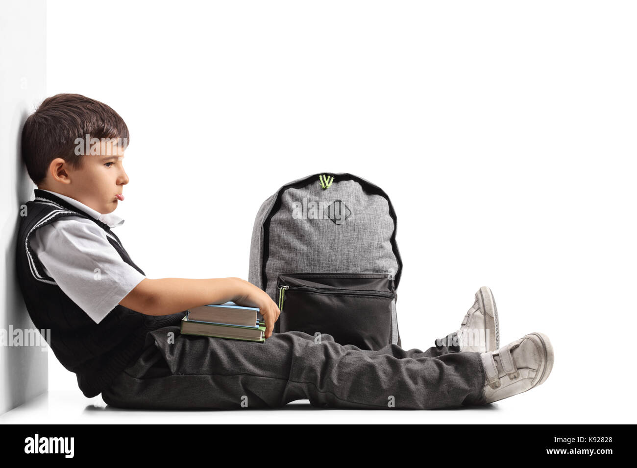 Sad schoolboy with a backpack and books seated on the floor isolated on ...