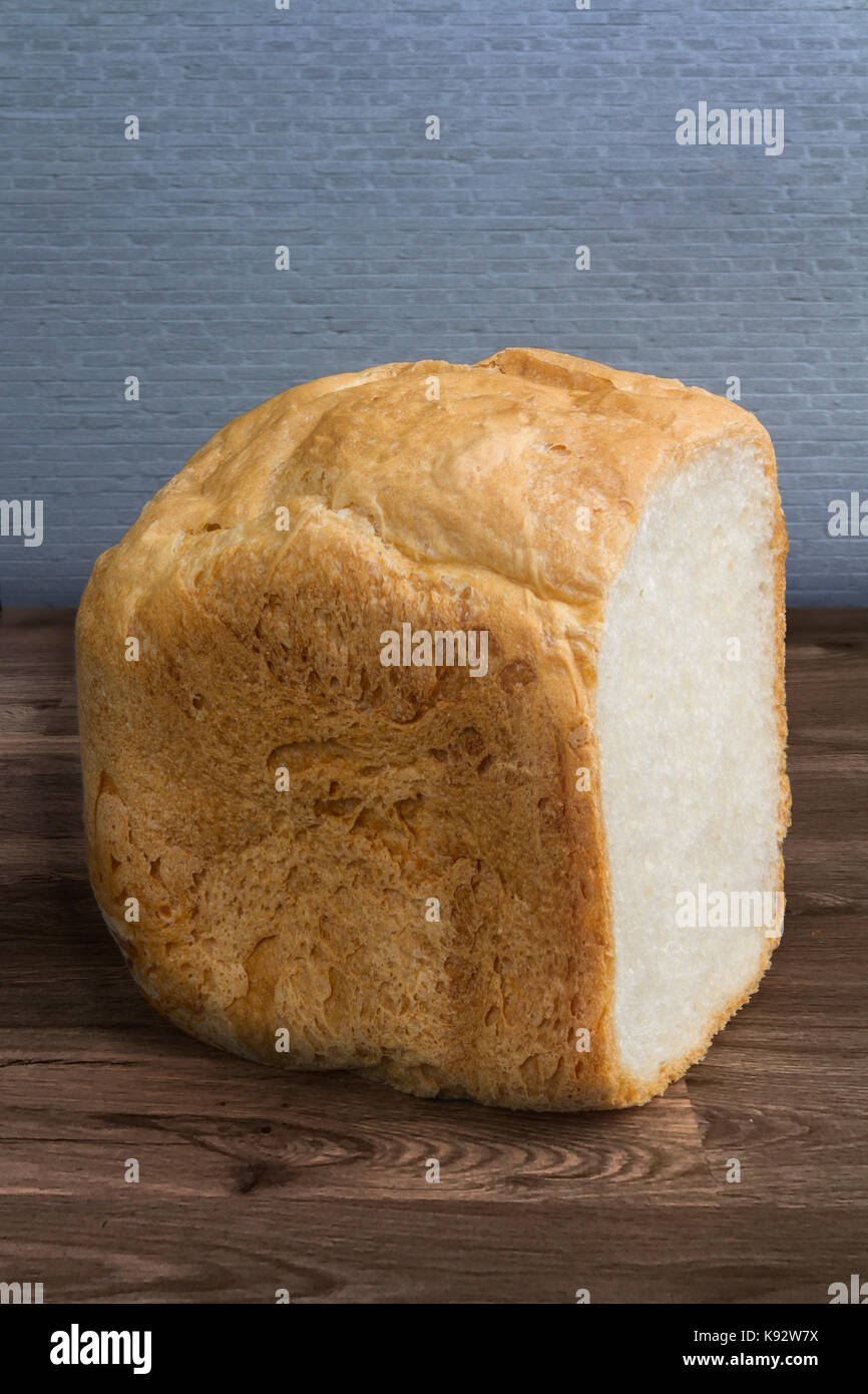 Hand baked and cut loaf of bread on a wooden bench by a grey painted ...