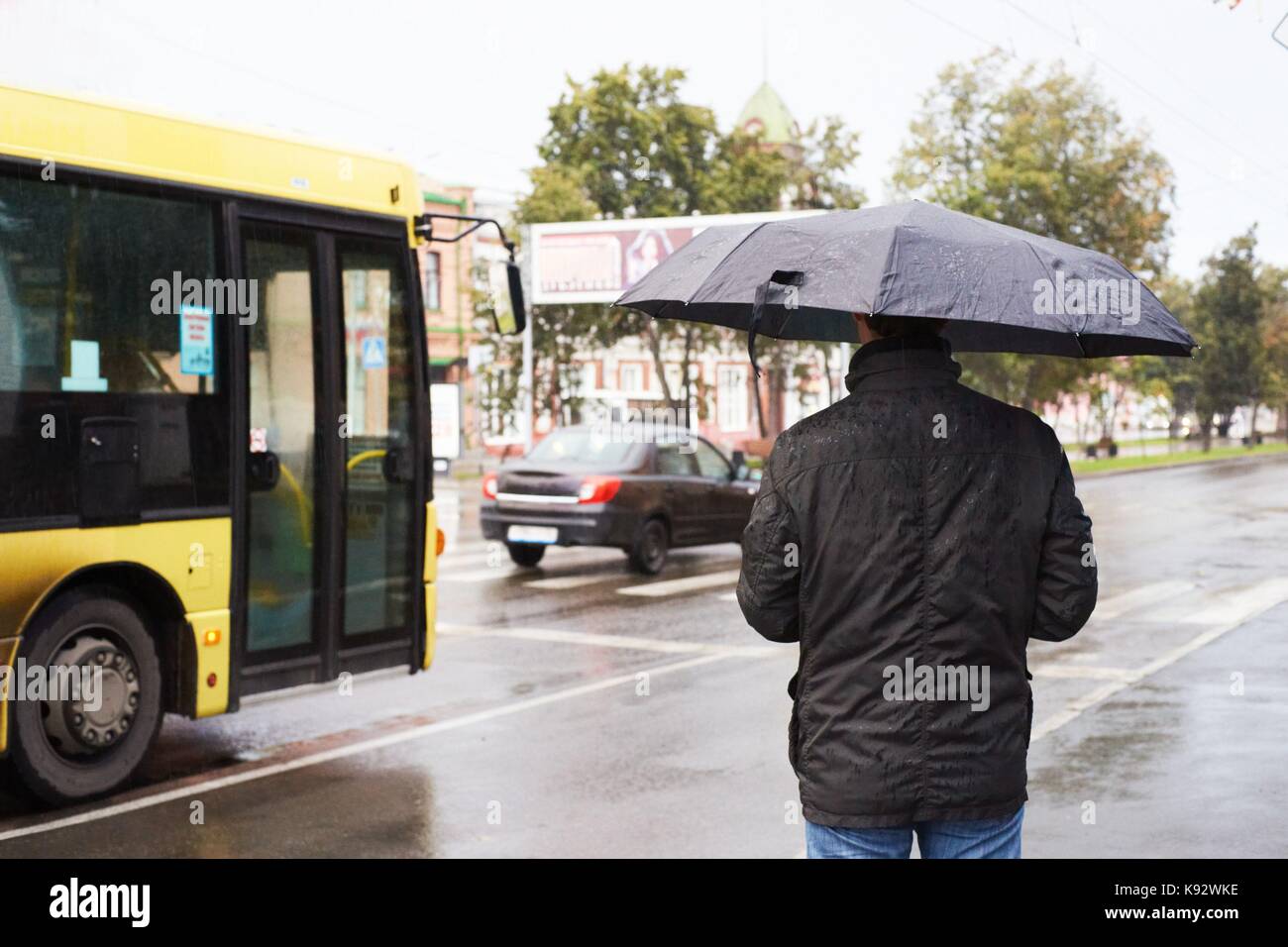 Man. Black umbrella. Yellow bus Stock Photo - Alamy