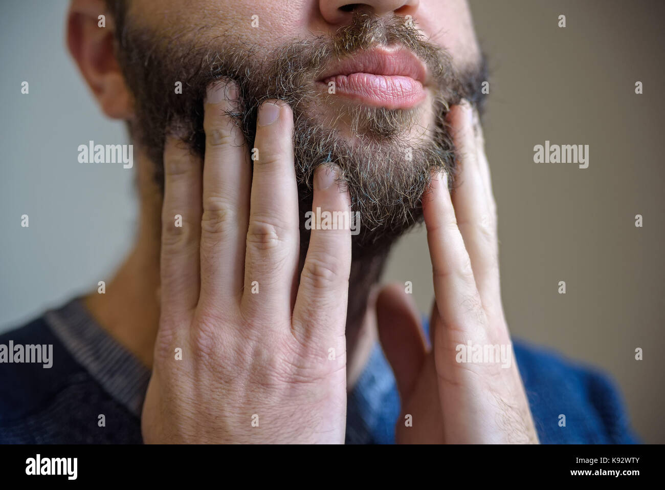 Close-up of young bearded man touching his beard while standing against ...