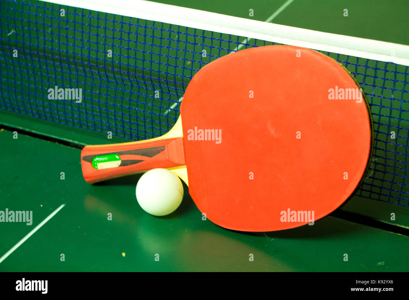 A red table tennis or ping pong racket and ball on a green table with ...