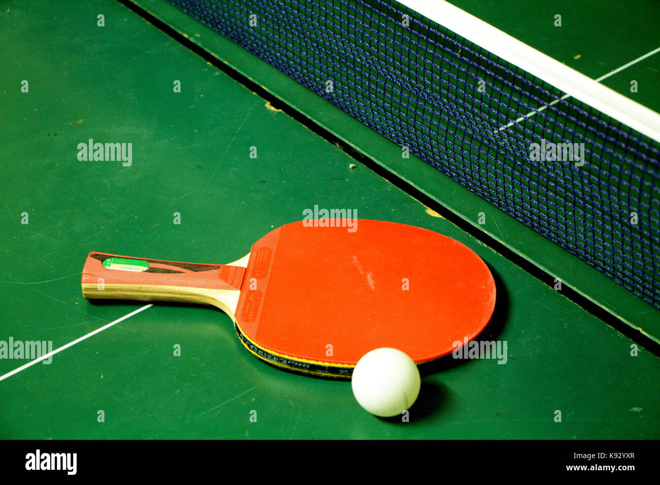 A table tennis or ping pong racket and ball on a green table with blue ...