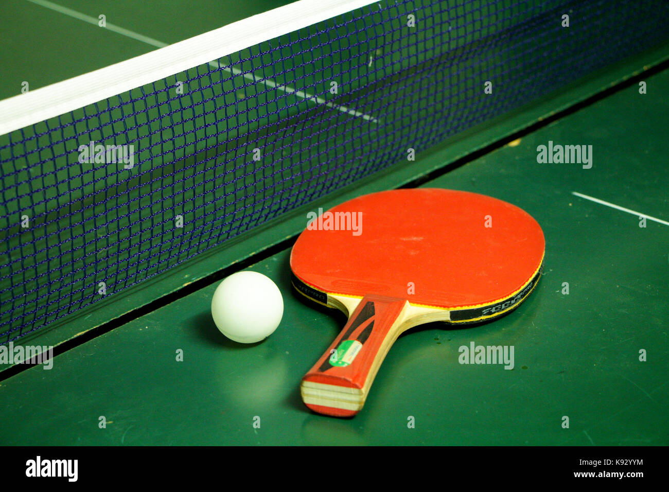 A red table tennis or ping pong racket and ball on a green table with ...